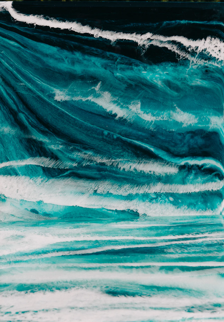 Layered teal and deep blue wave textures sweep diagonally across the frame, with foamy white bands breaking through the surface. The scene feels like an abstract aerial view of the sea.