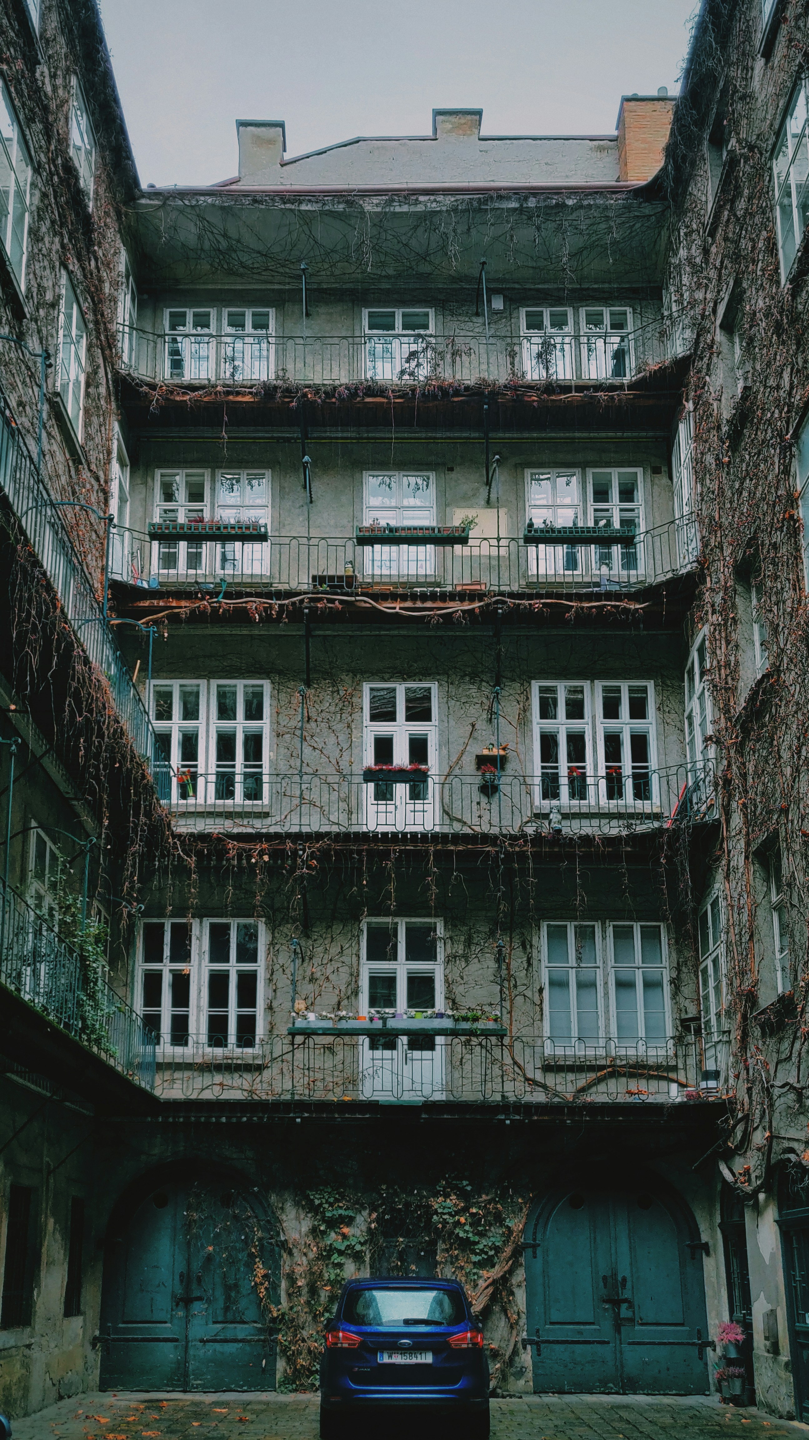 Crozen Courtyard: A Blue Car Beneath Ivy-Wrapped Balconies