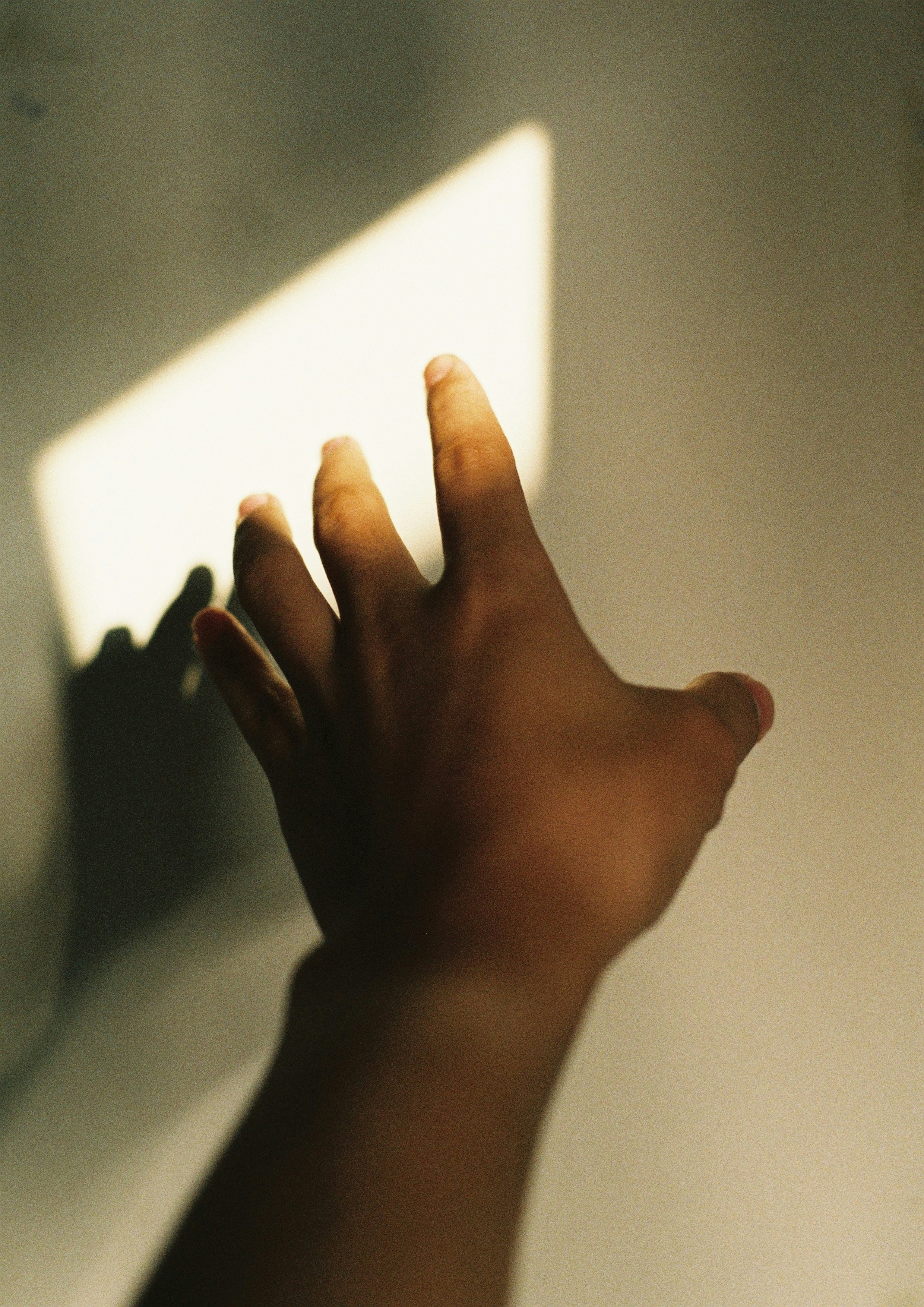 Fingers in Light: A Hand Reaches Toward a Rectangular Beam on a Quiet Wall