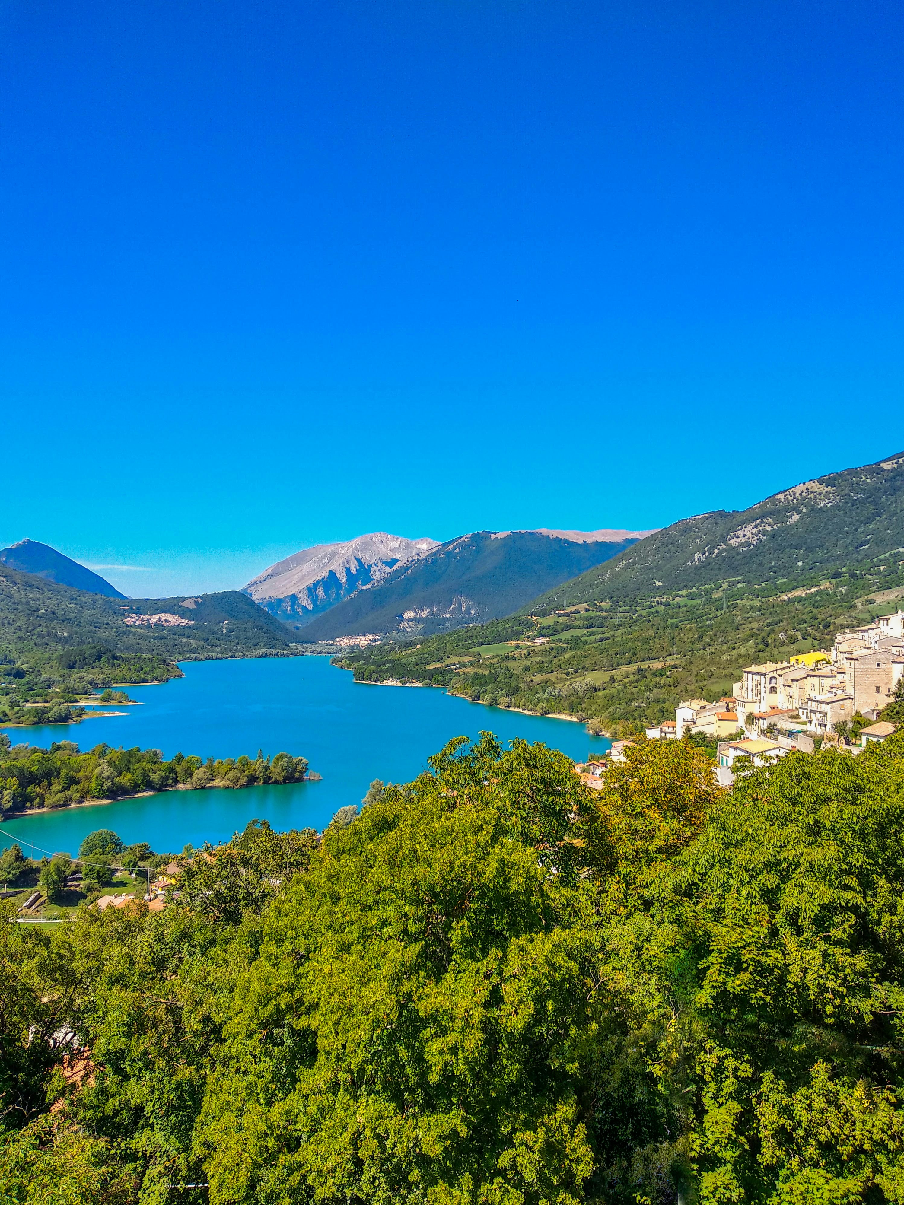 Lush greenery frames a tranquil lake surrounded by mountains, showcasing a harmonious blend of nature's beauty and human habitation.