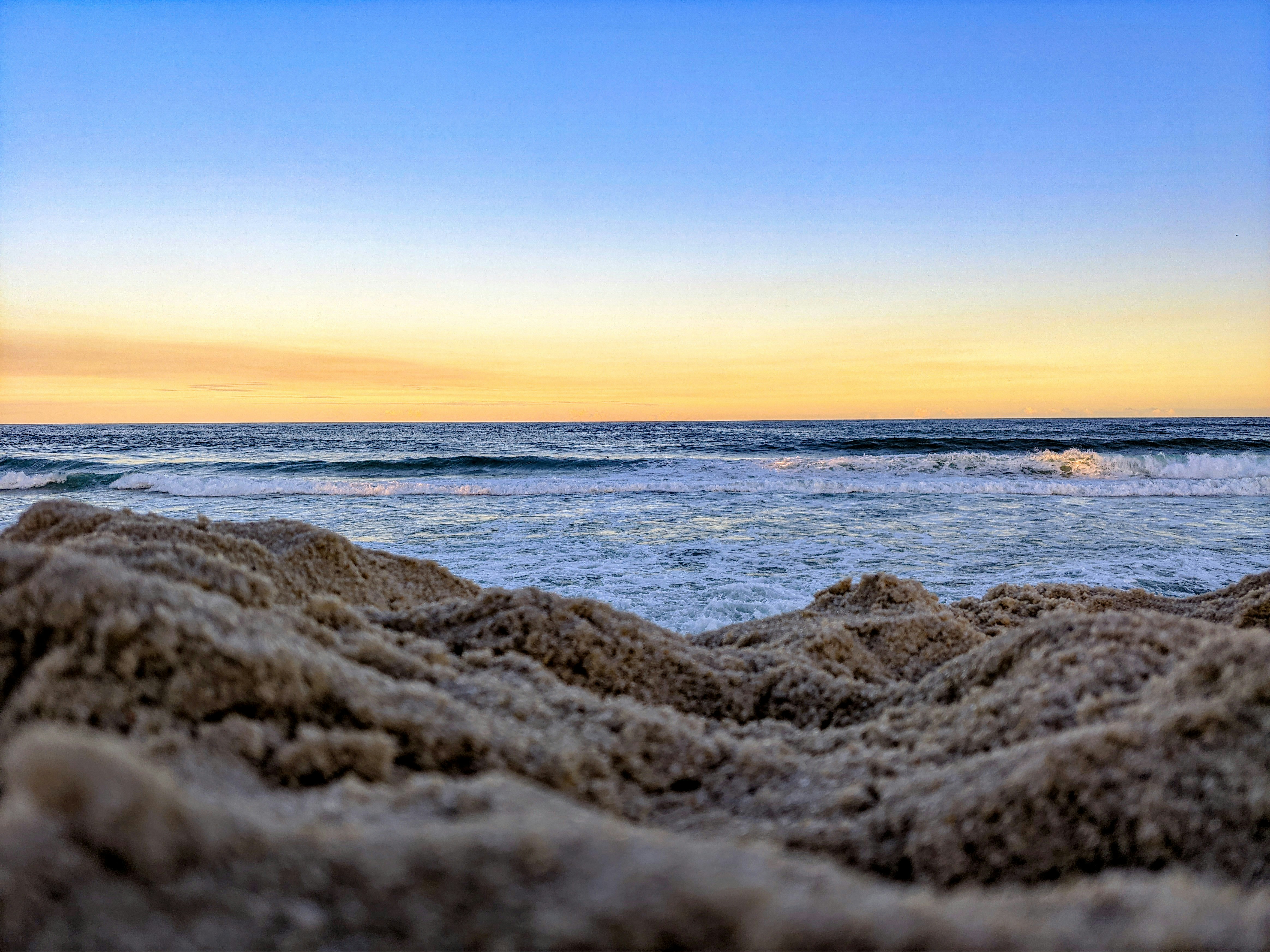 Golden sunset over the ocean with textured sandy foreground.