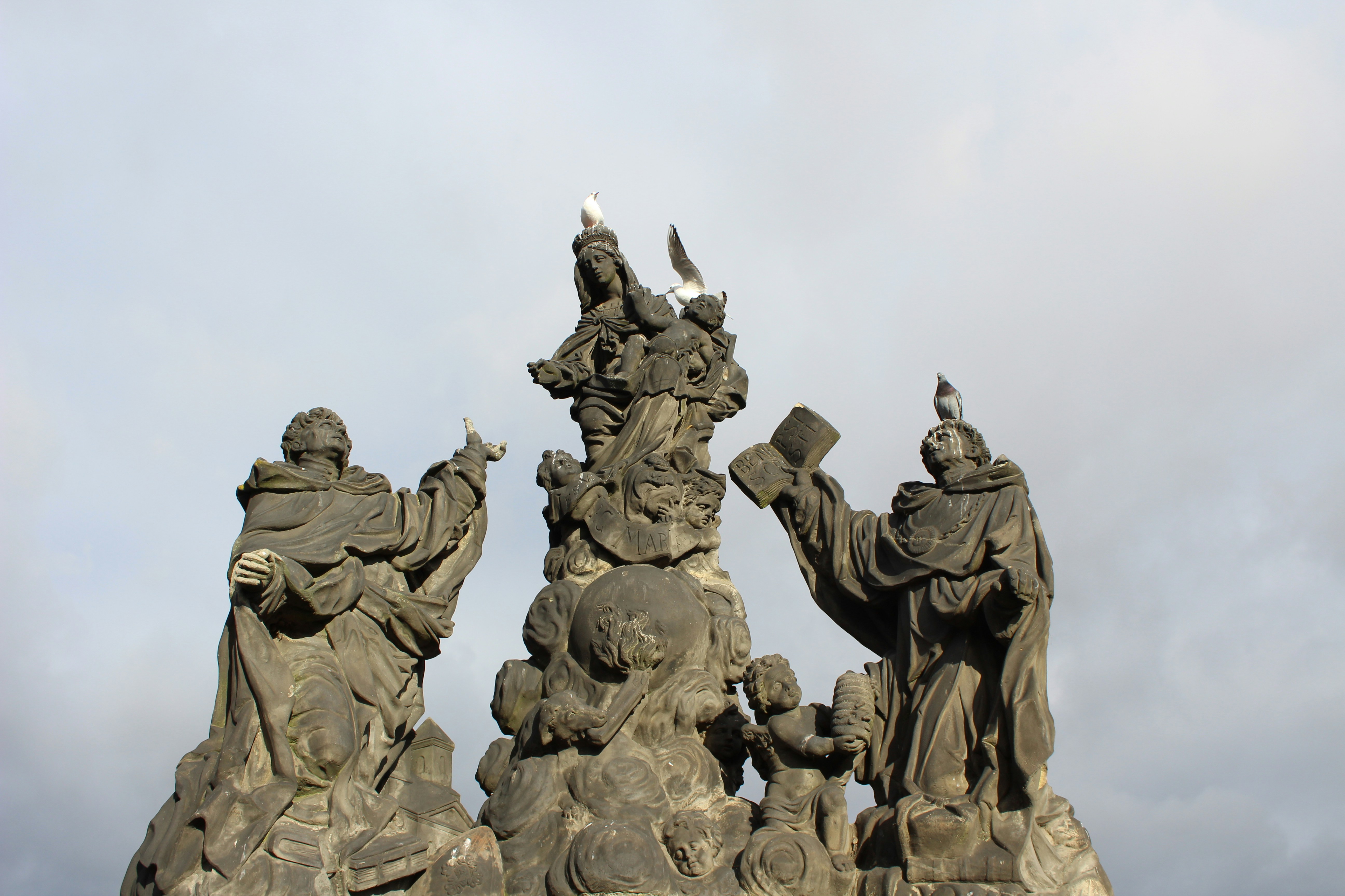 Ornate stone statues topped with perched birds against a cloudy sky.