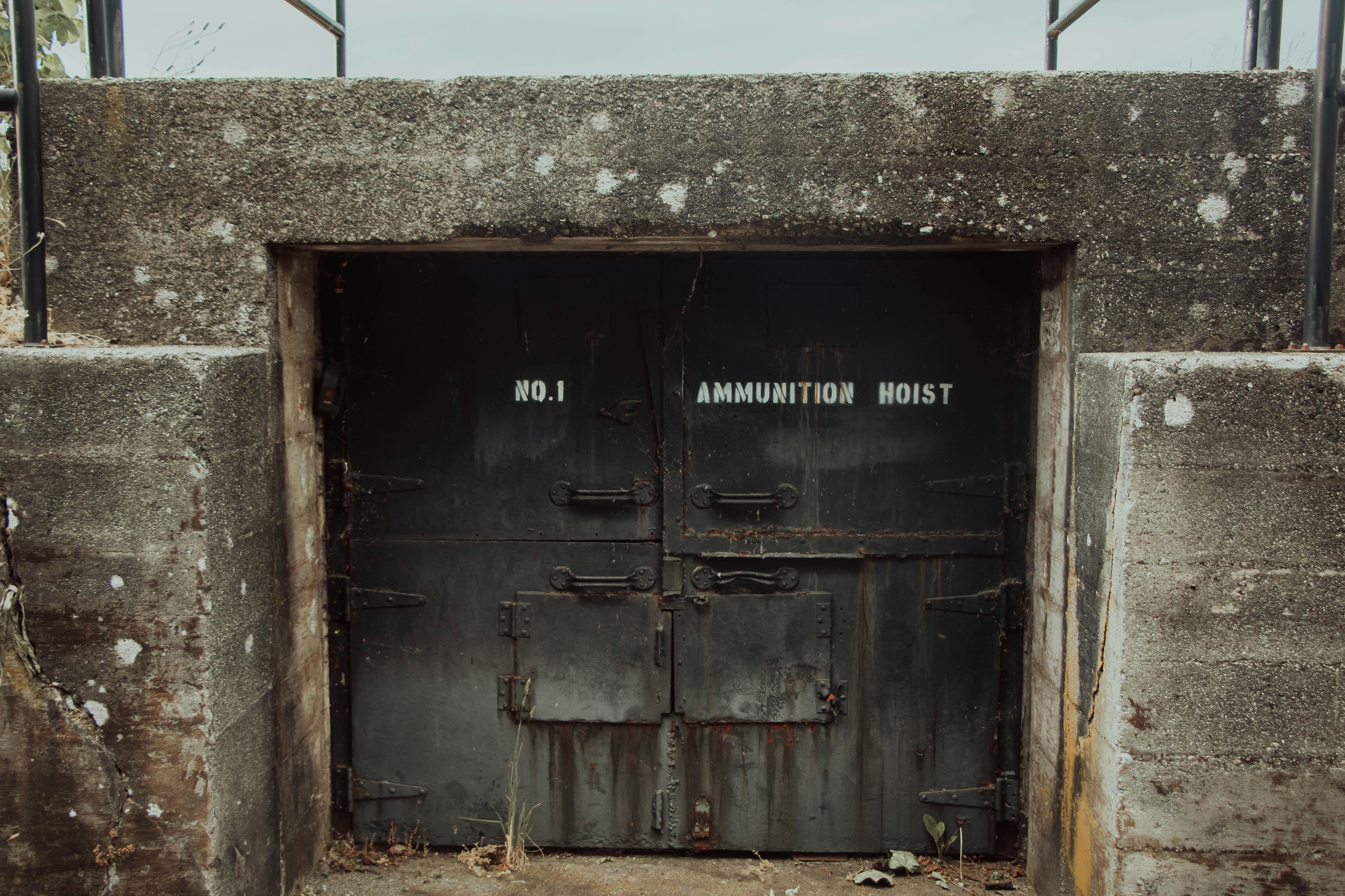 Weathered metal doors labeled 'NO. 1 AMMUNITION HOIST' reveal remnants of a bygone era, framed by rugged concrete. The scene evokes a sense of mystery and nostalgia.