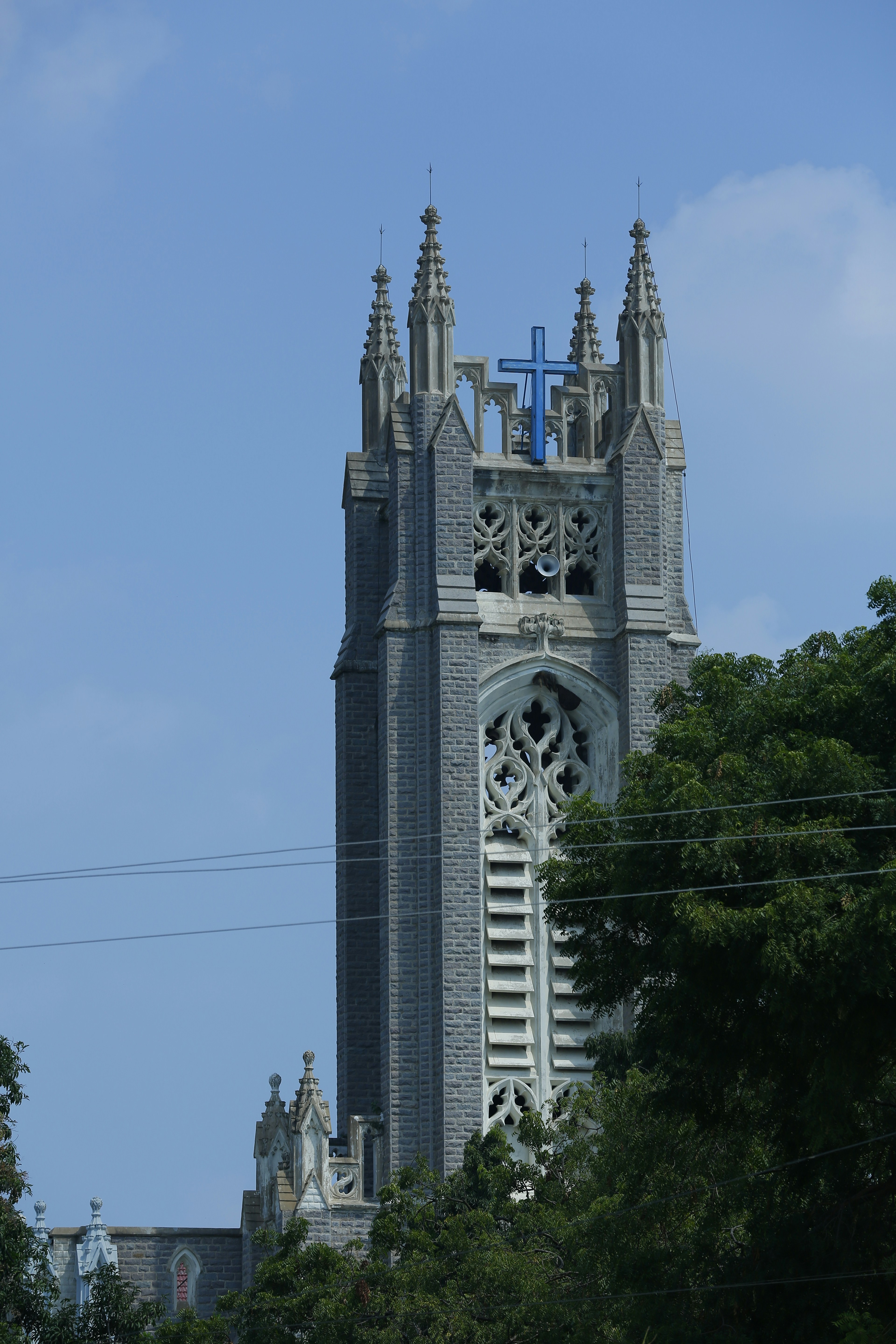 Gothic-style church tower adorned with intricate stonework and a prominent cross against a clear blue sky.