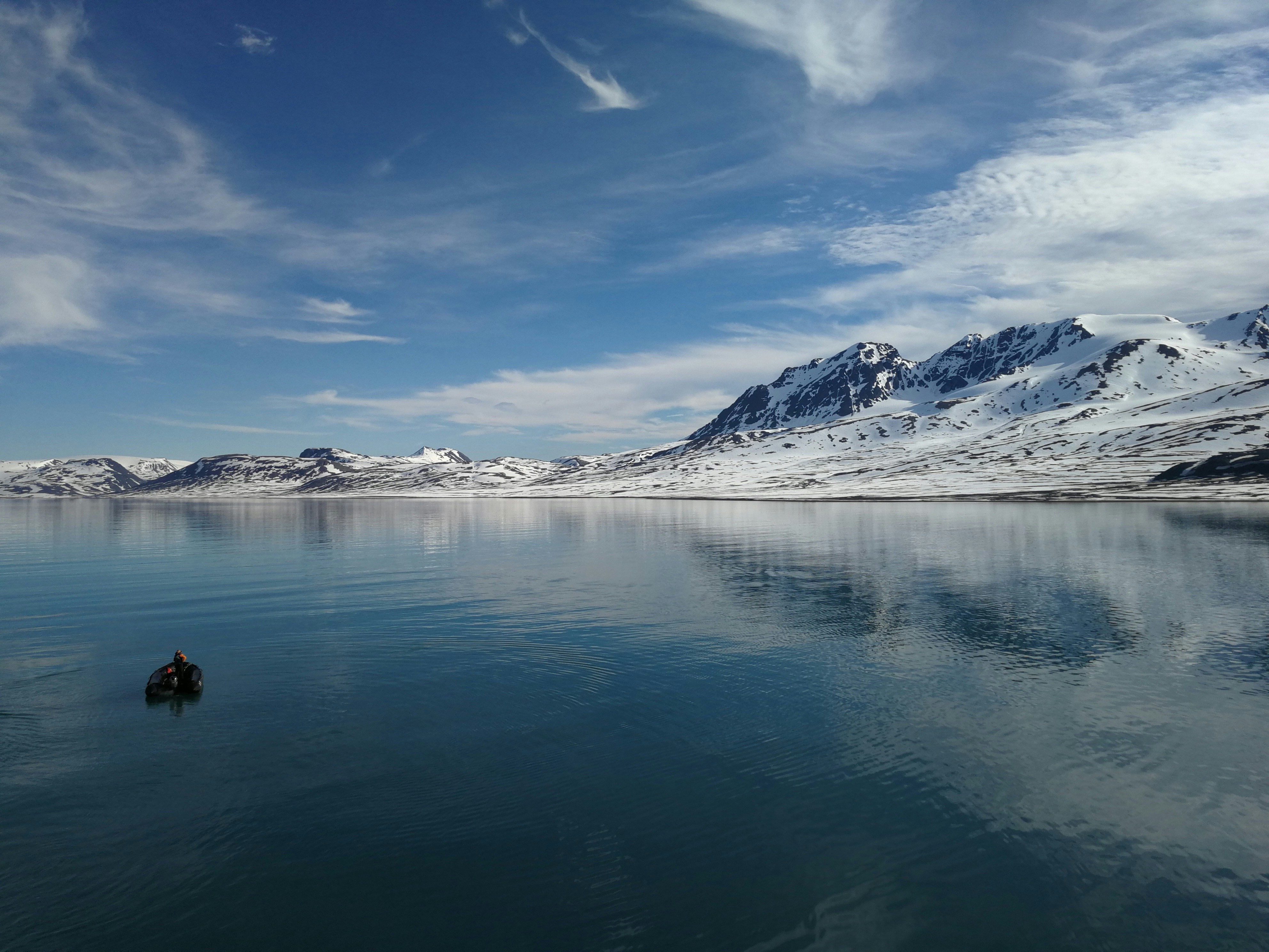 A solitary figure in a kayak glides across a tranquil, icy blue lake, surrounded by majestic snow-covered mountains under a clear sky.