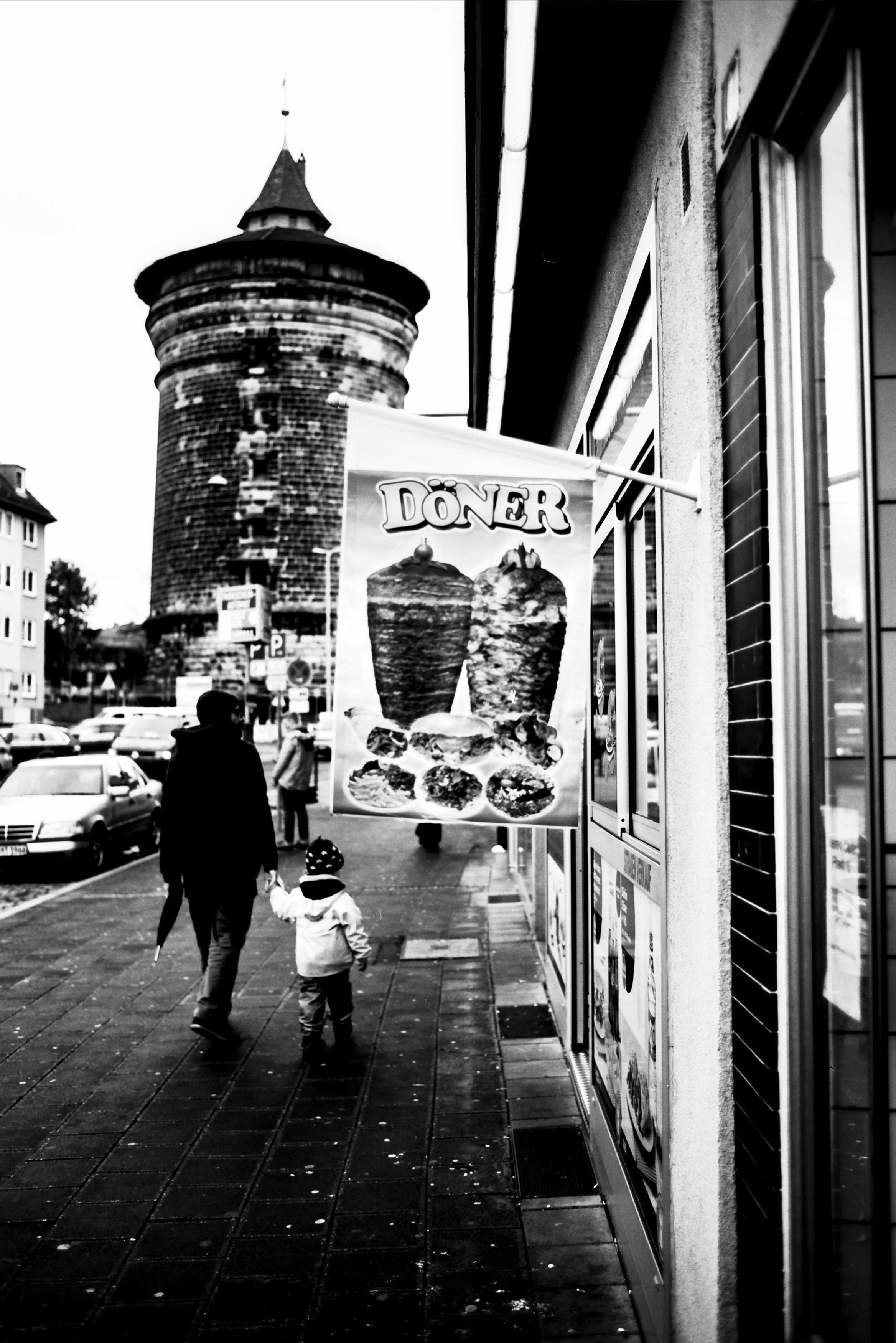 Street front with towering kebab sign and a child’s first steps toward the city