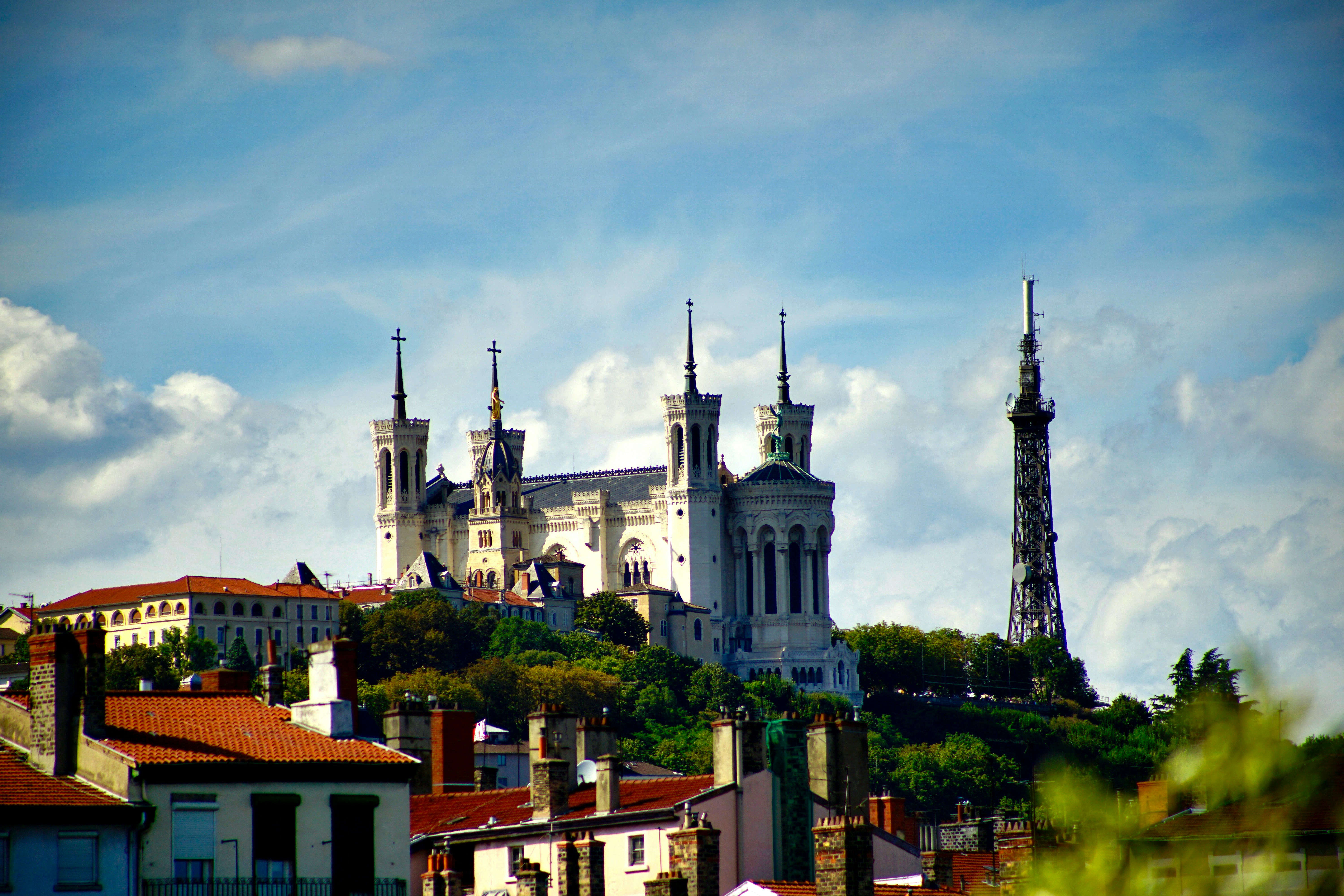 Historic cathedral with ornate spires and an adjacent tower set on a lush hill under a vibrant blue sky.