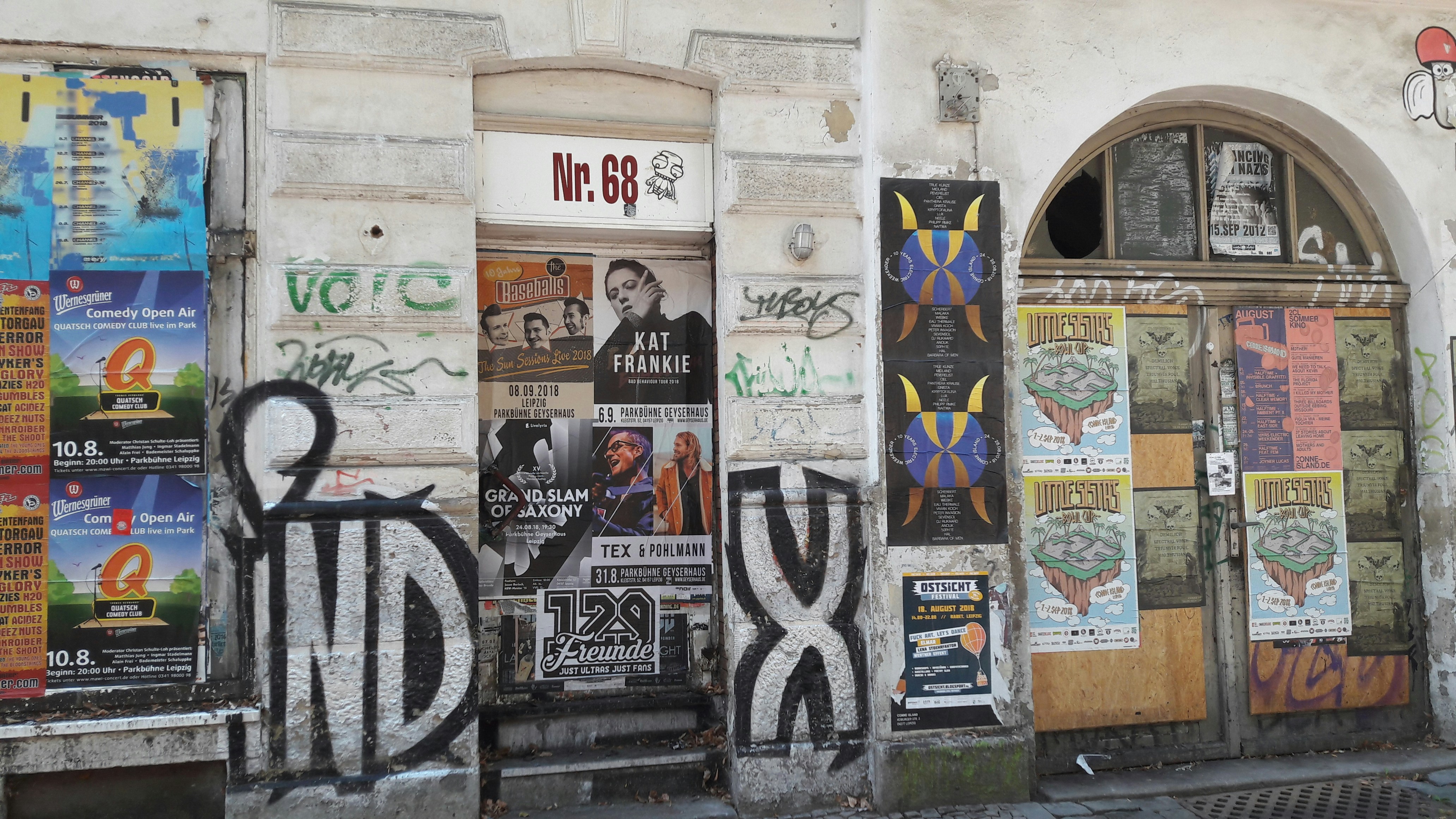 Graffiti-covered wall featuring high doors plastered with vibrant posters in an urban setting.