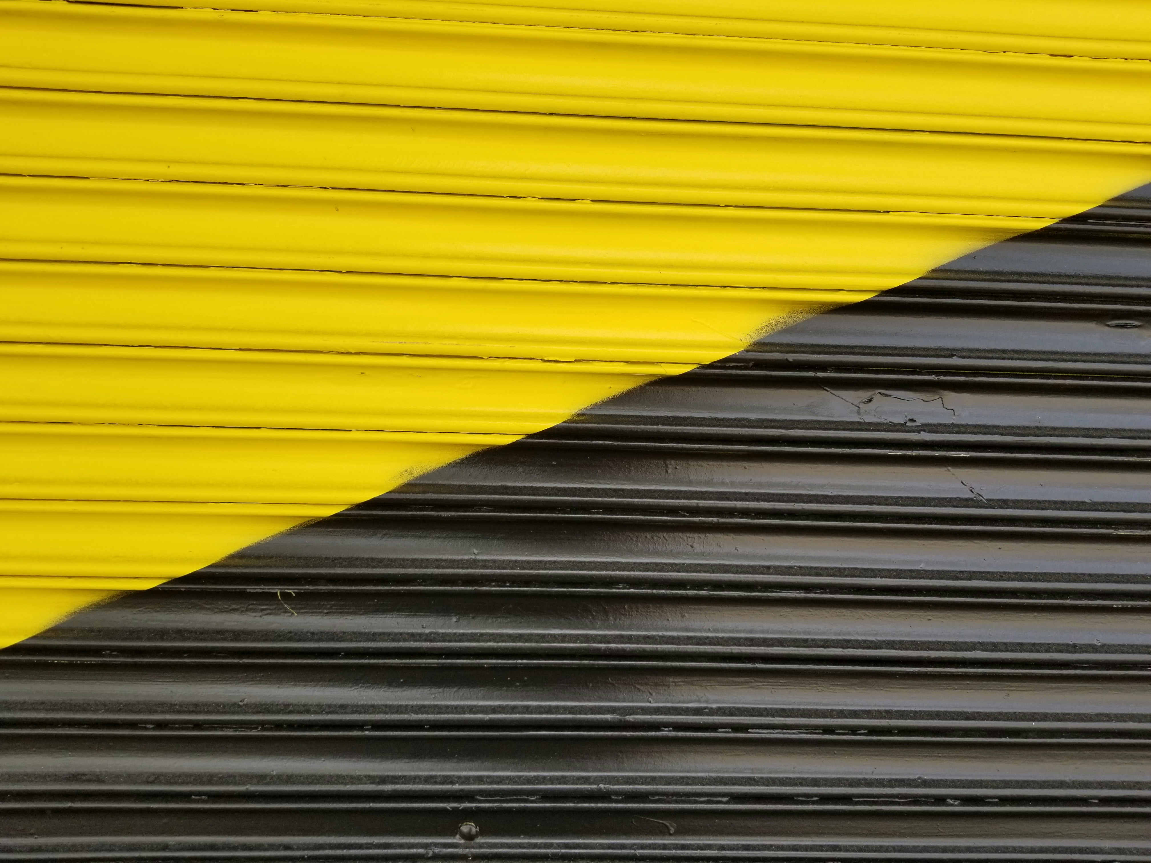 Close-up of a two-tone corrugated roller shutter with a bold yellow diagonal segment against black.