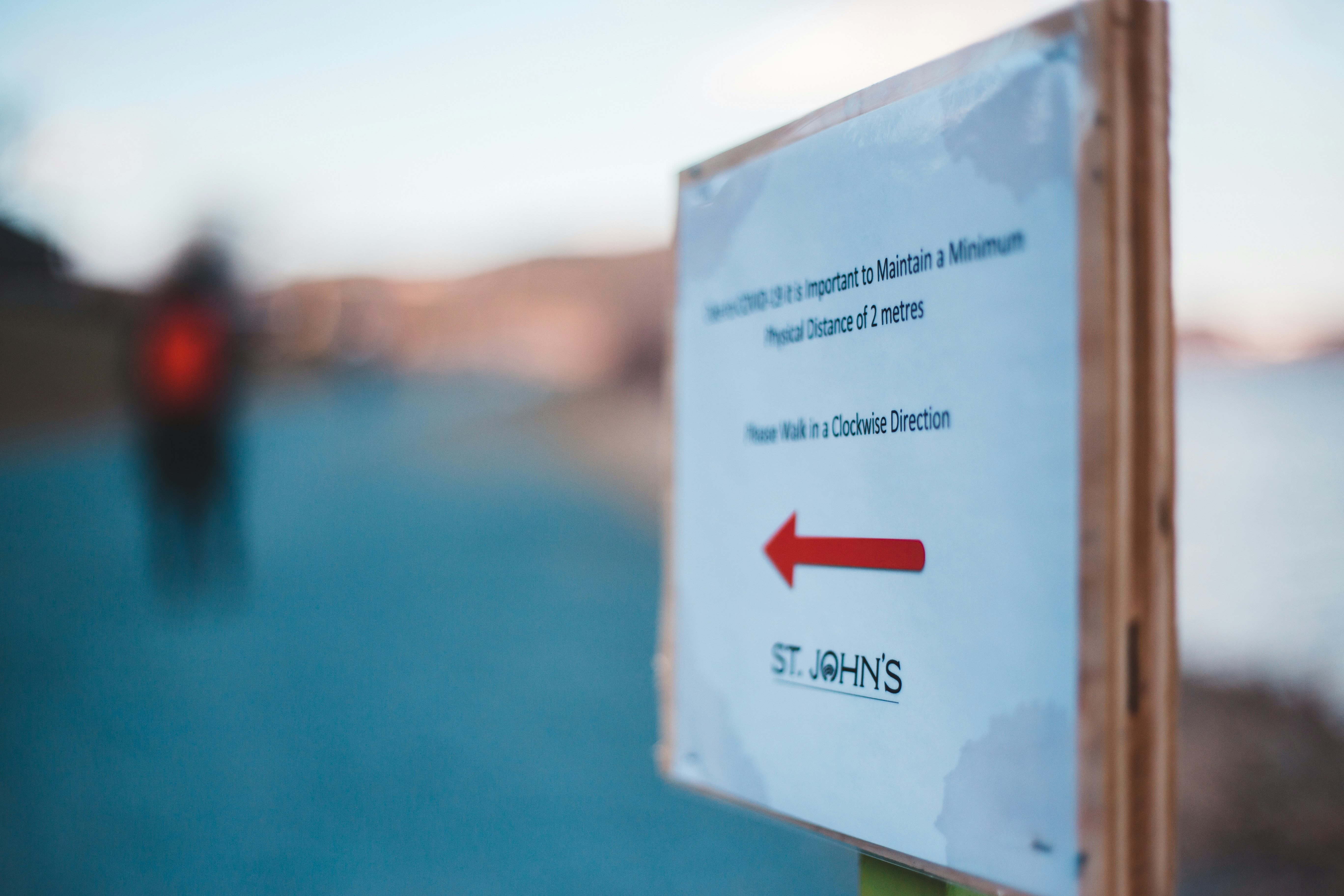 Directional sign instructing pedestrians to maintain distance and walk in a clockwise direction along a scenic pathway.