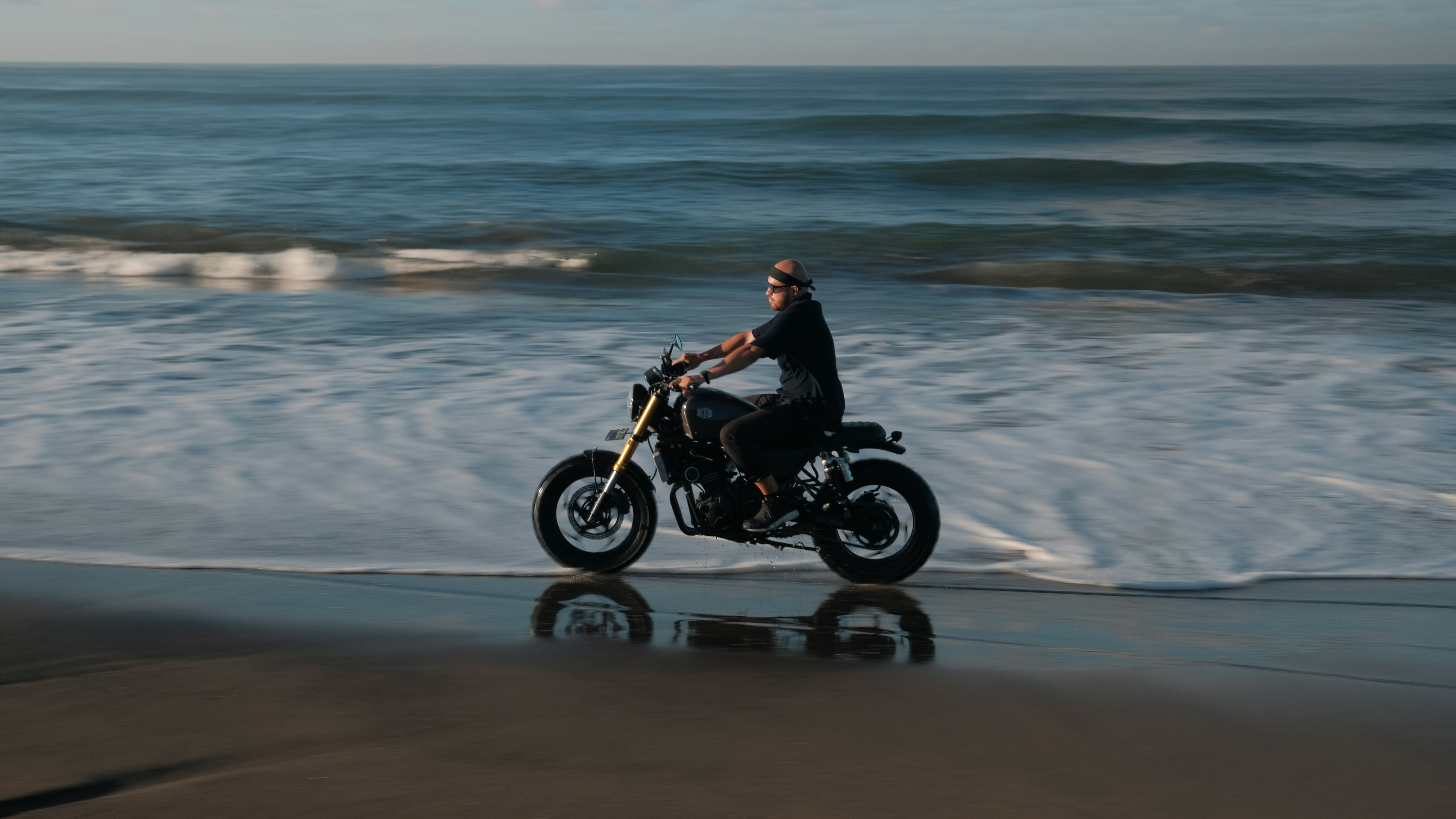 Motorcyclist navigating the shoreline, with waves gently crashing at the beach. The scene captures the essence of adventure and the beauty of coastal landscapes.