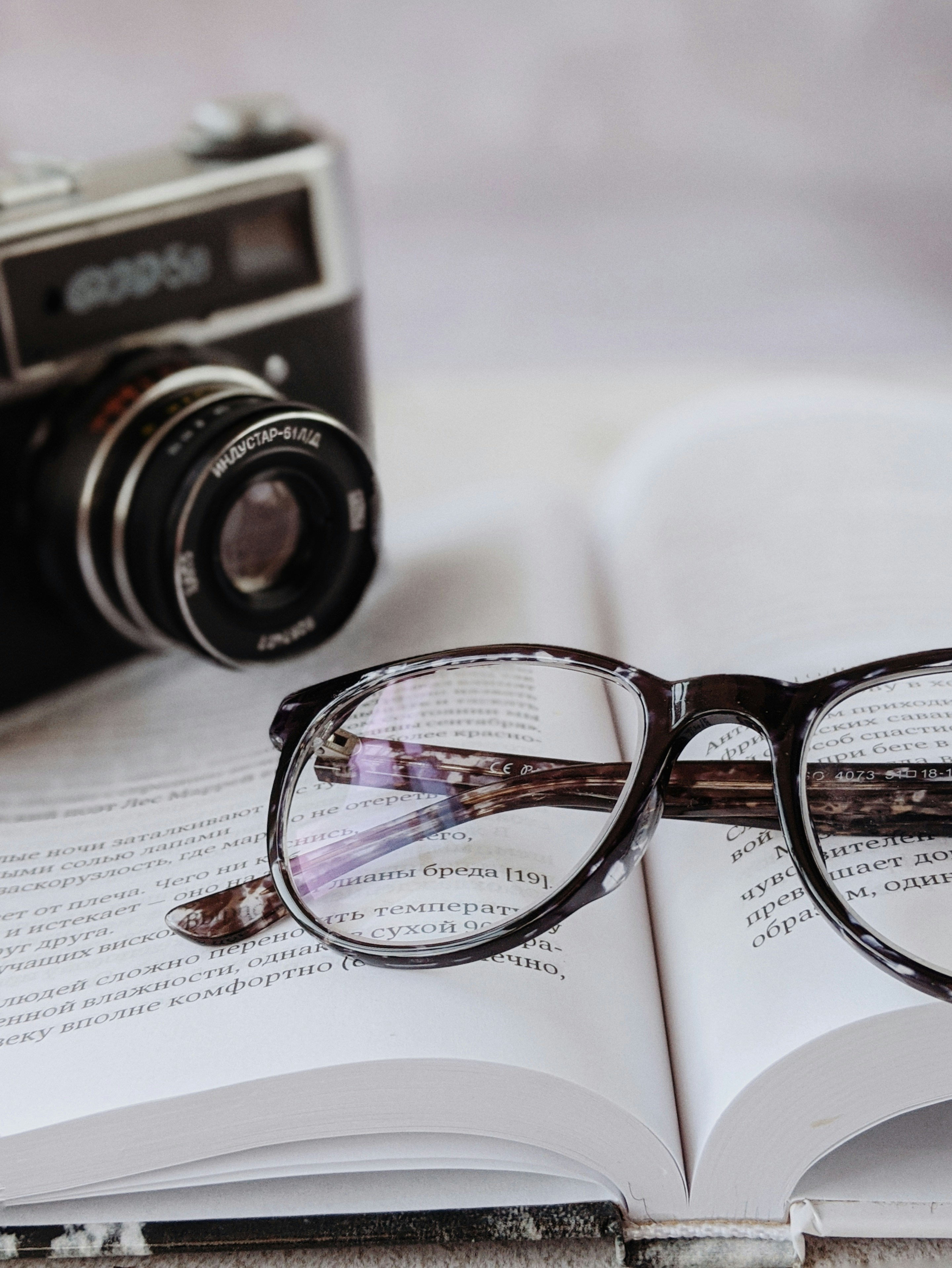 Vintage camera resting beside a pair of glasses on an open book, illustrating a blend of nostalgia and intellect.