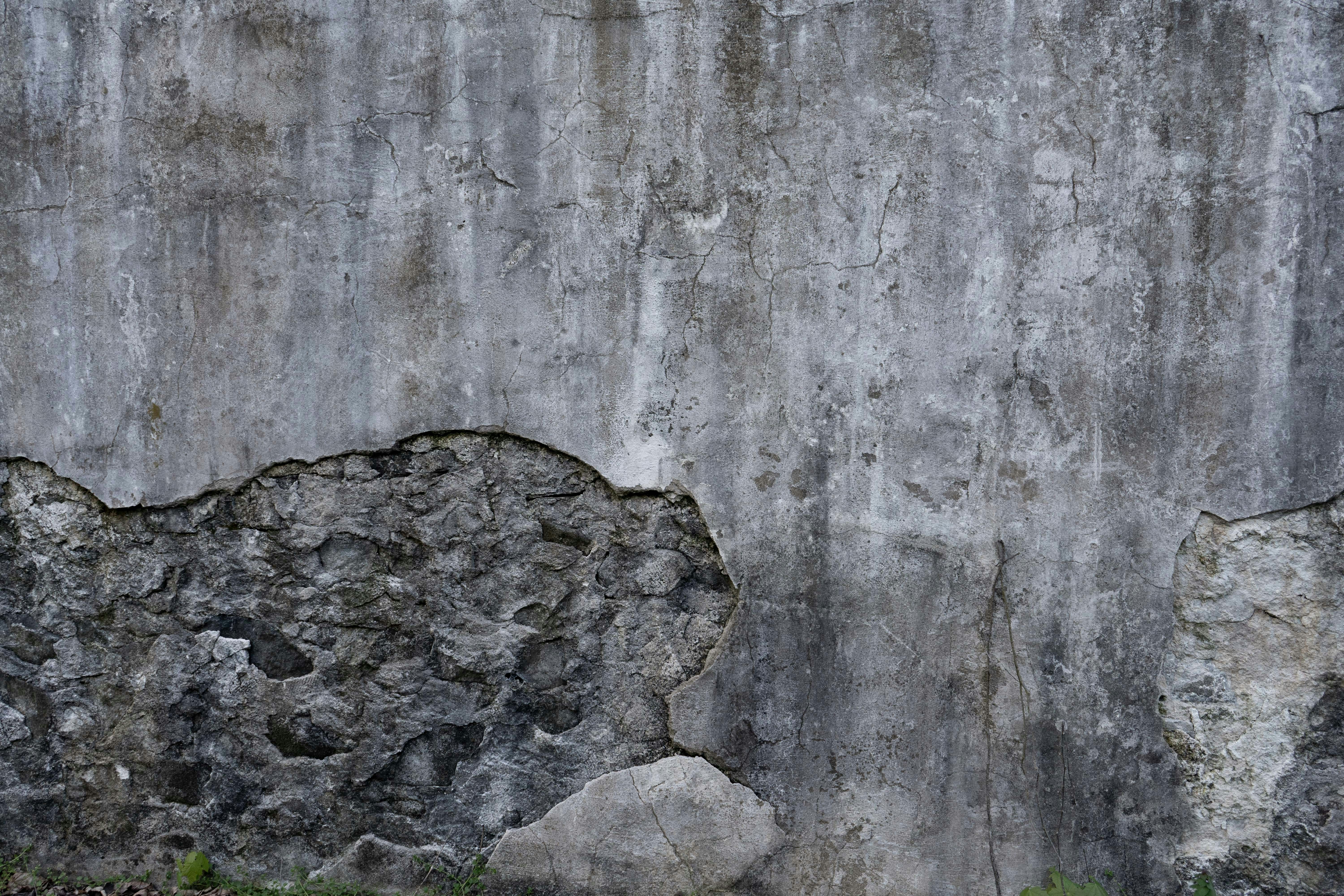 Textured concrete wall revealing layers of weathered stone and plaster, showcasing the passage of time.