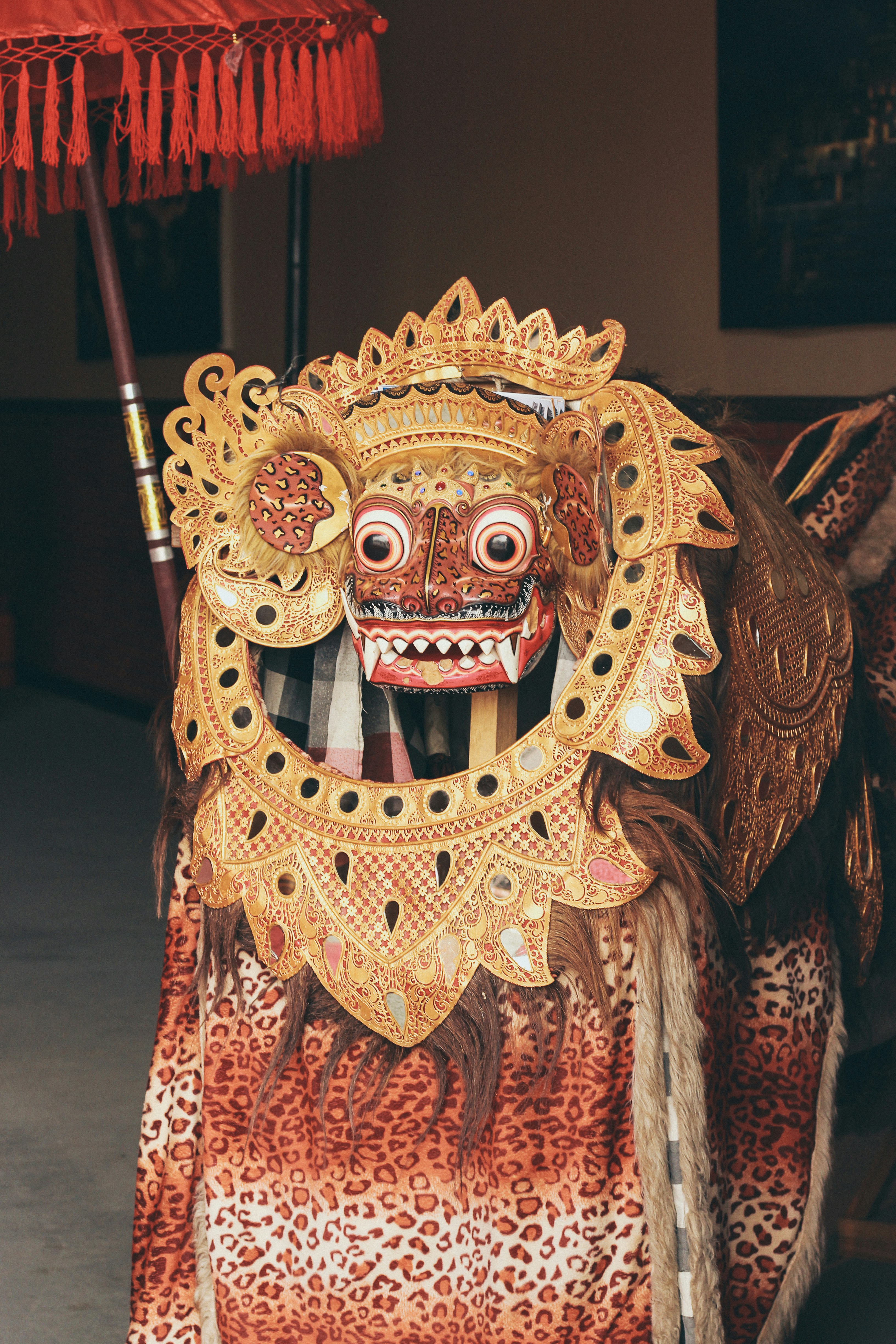 Elaborately adorned lion mask with vibrant colors and intricate patterns, symbolizing cultural heritage. A red parasol enhances the festive atmosphere.
