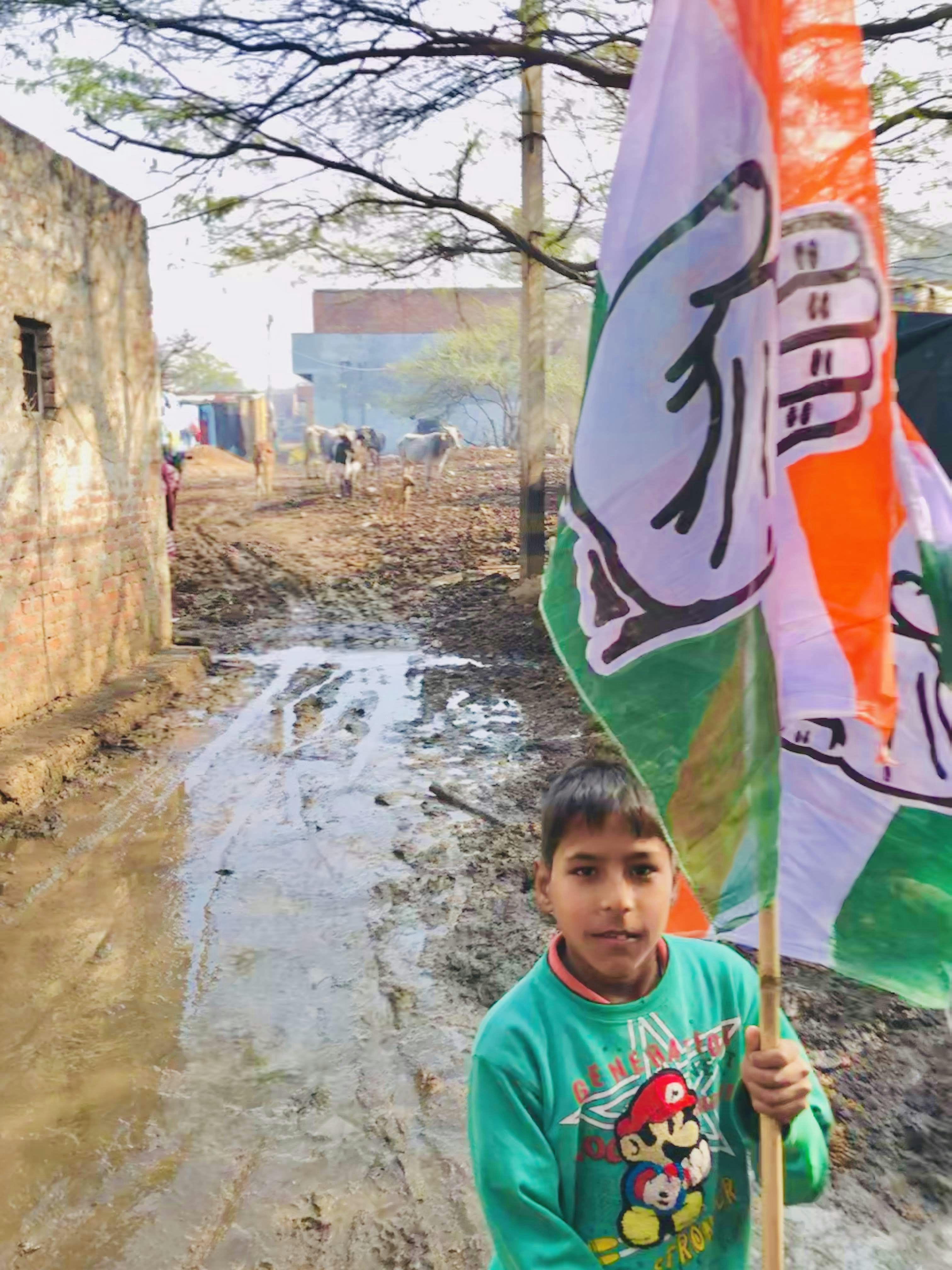 Flag Bearer in a Muddy Village Lane Under Morning Light