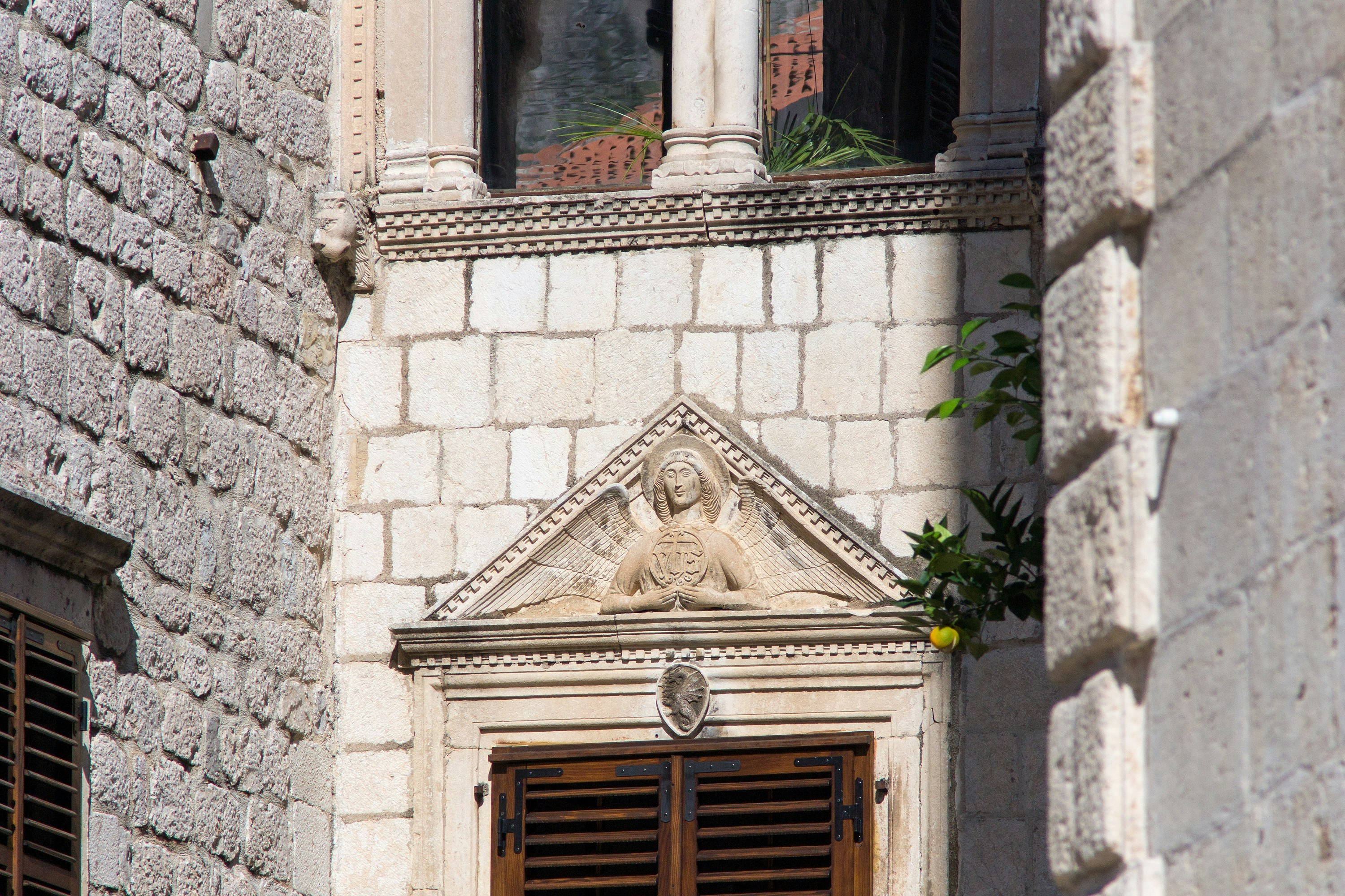 Intricate stone relief of a figure set above a wooden window, framed by textured stone walls in a historic setting.