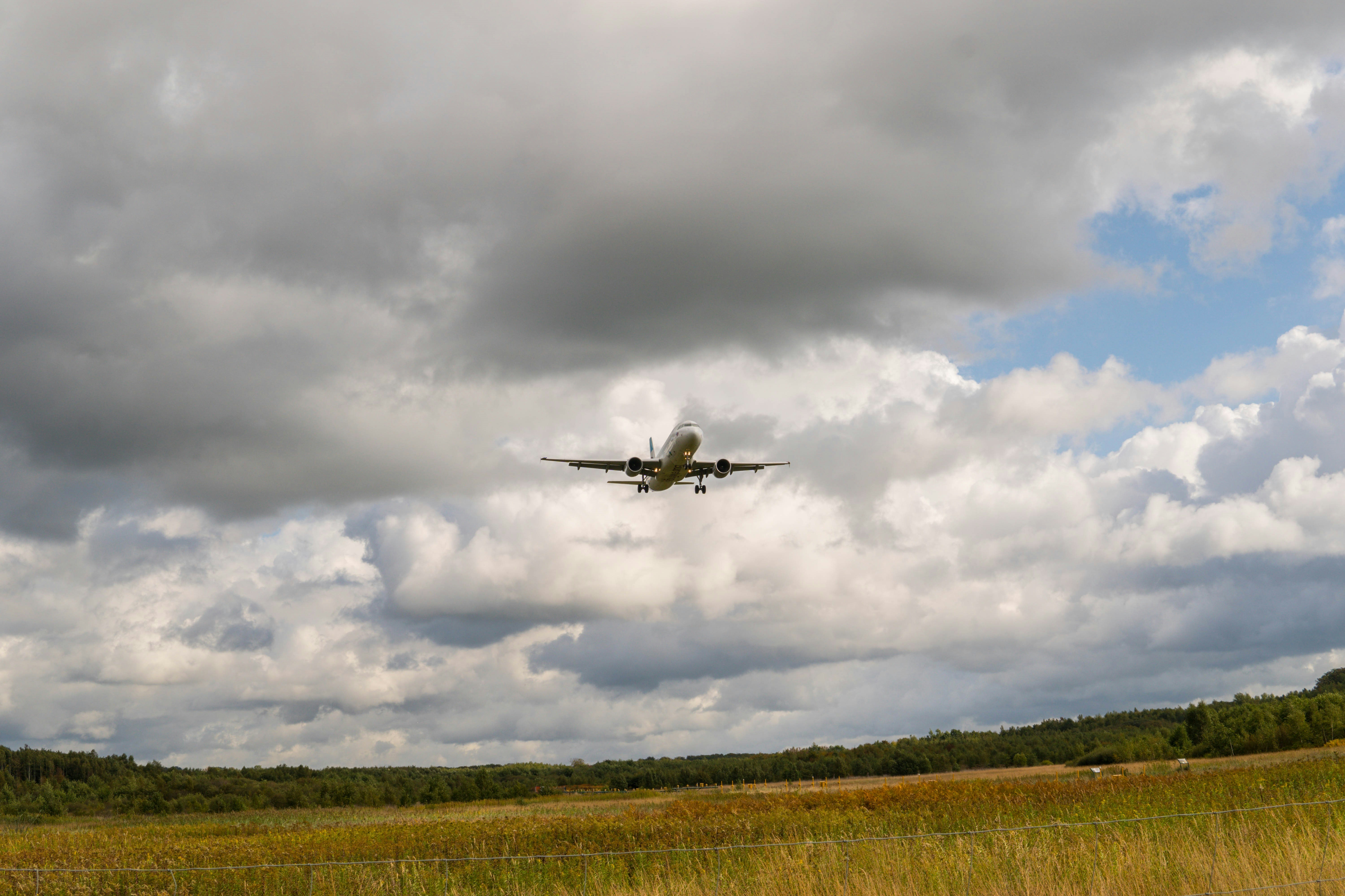 Airbus descending over a grassy field under a dramatic sky filled with clouds.
