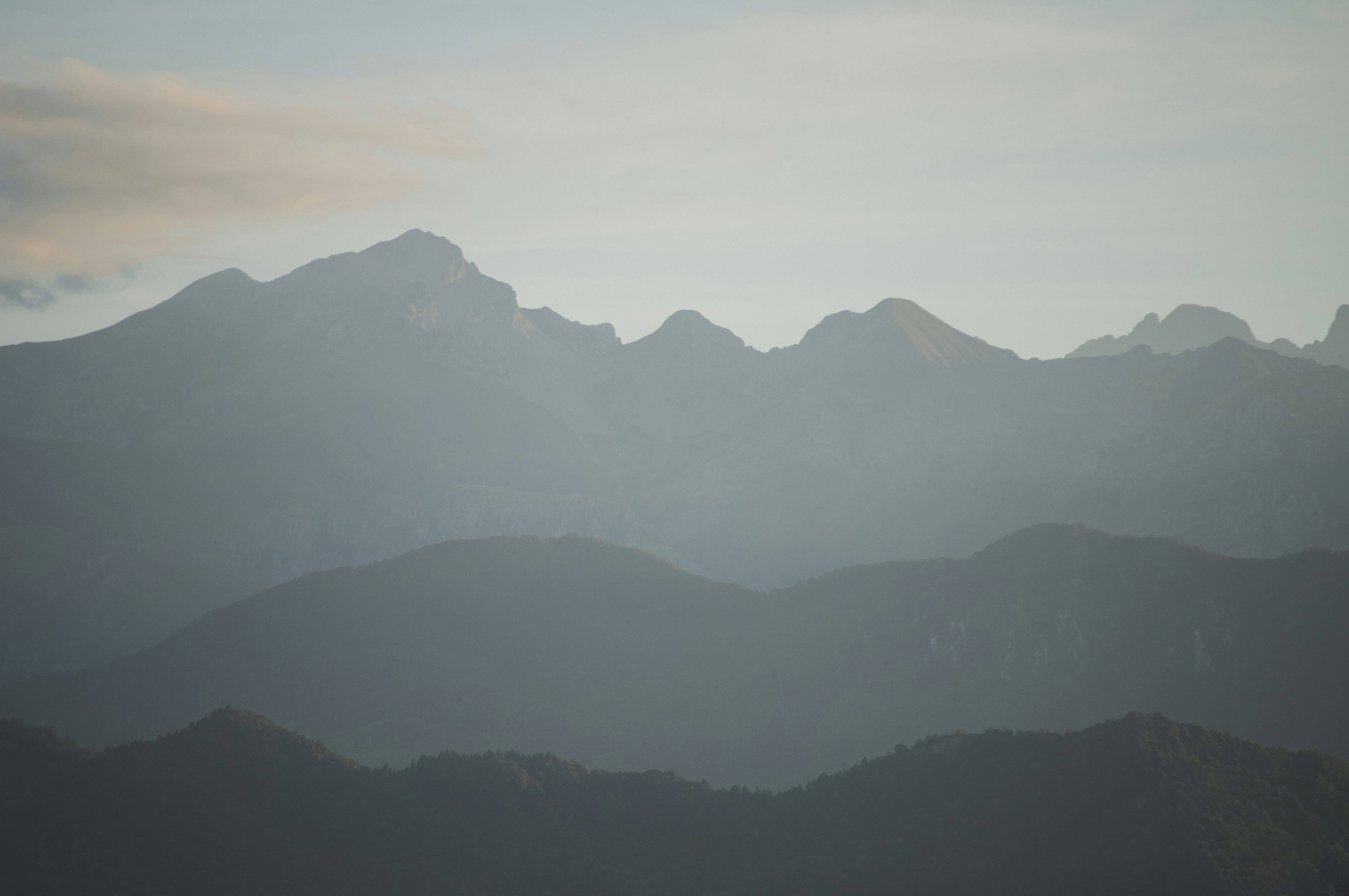 Layered silhouettes of distant mountains under a soft, hazy sky, evoking a sense of tranquility and depth.