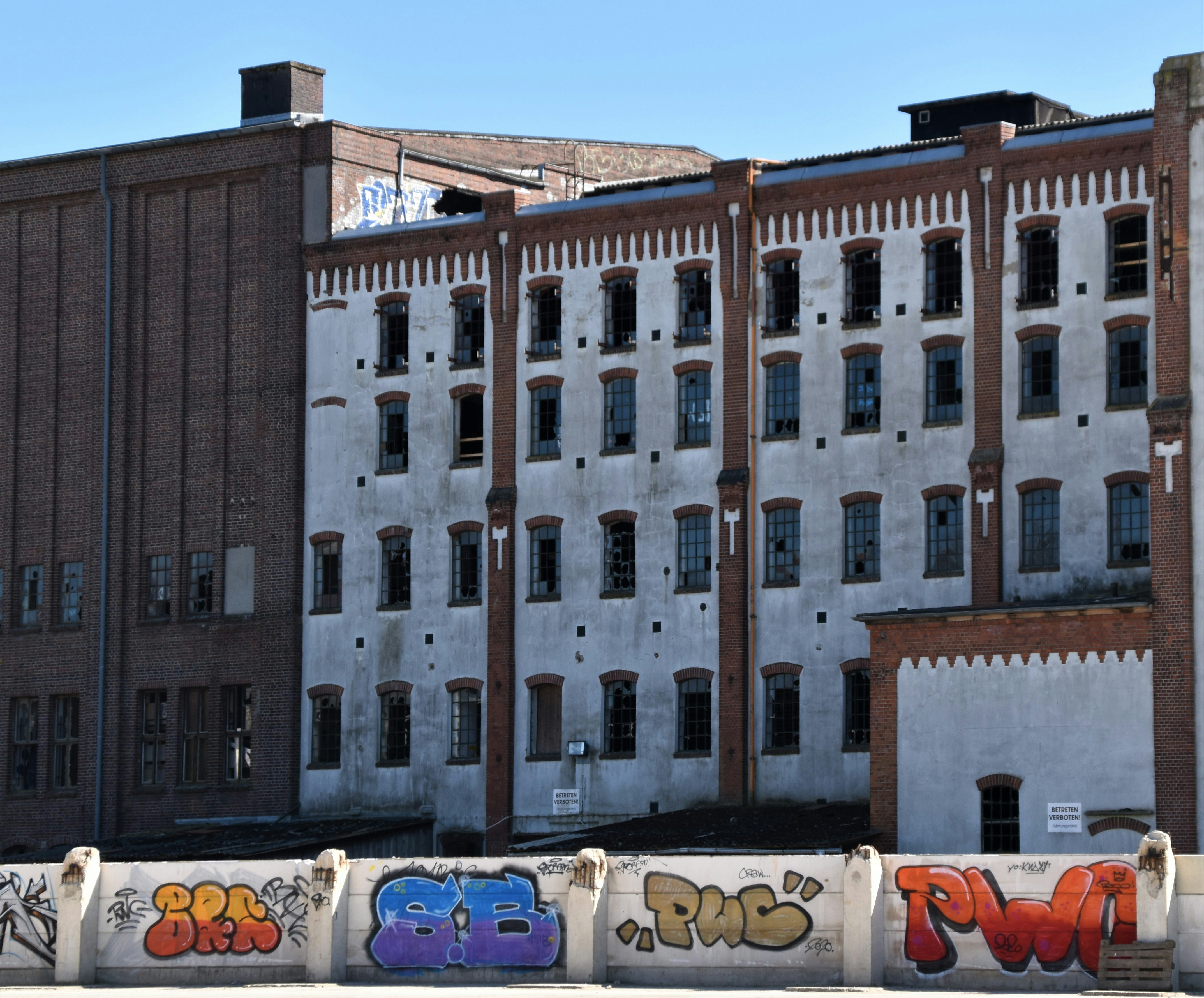 Abandoned warehouse facade adorned with vibrant graffiti, showcasing urban art against a backdrop of weathered brick and broken windows.
