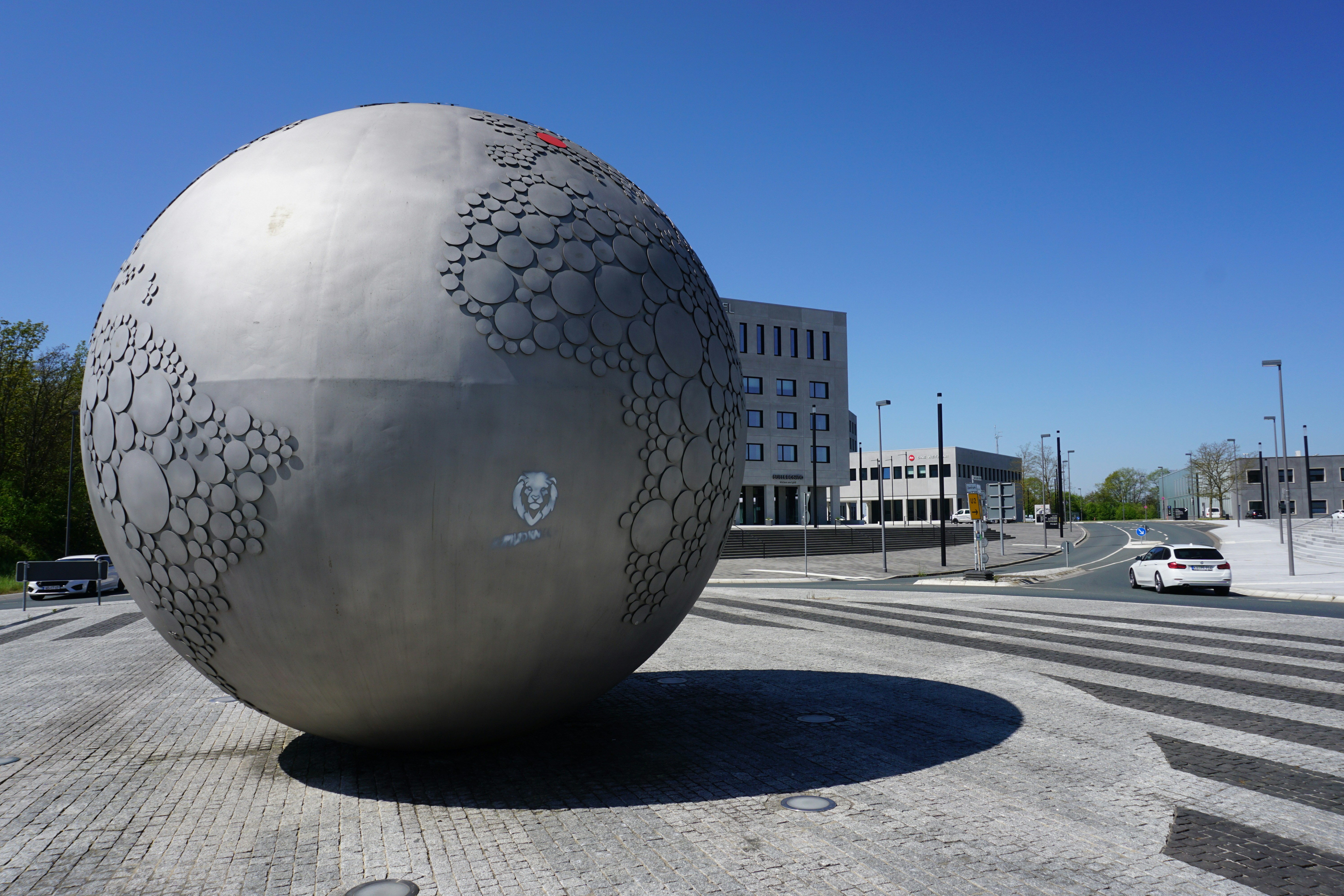 World-Headquarter of Leica Camera AG in Wetzlar, called Leitz-Park Campus, with Leica Cine Wetzlar, production site of world class cinema lenses, Ernst Leitz Hotel and a huge globe. My interpretation: The World seen through many (grey) eyes / circles with one red eye / circle located in middle Europe / Wetzlar. Meaning: Many see the world, but the red hotspot of photography is Leicas' Wetzlar with the red dot Leica logo.
