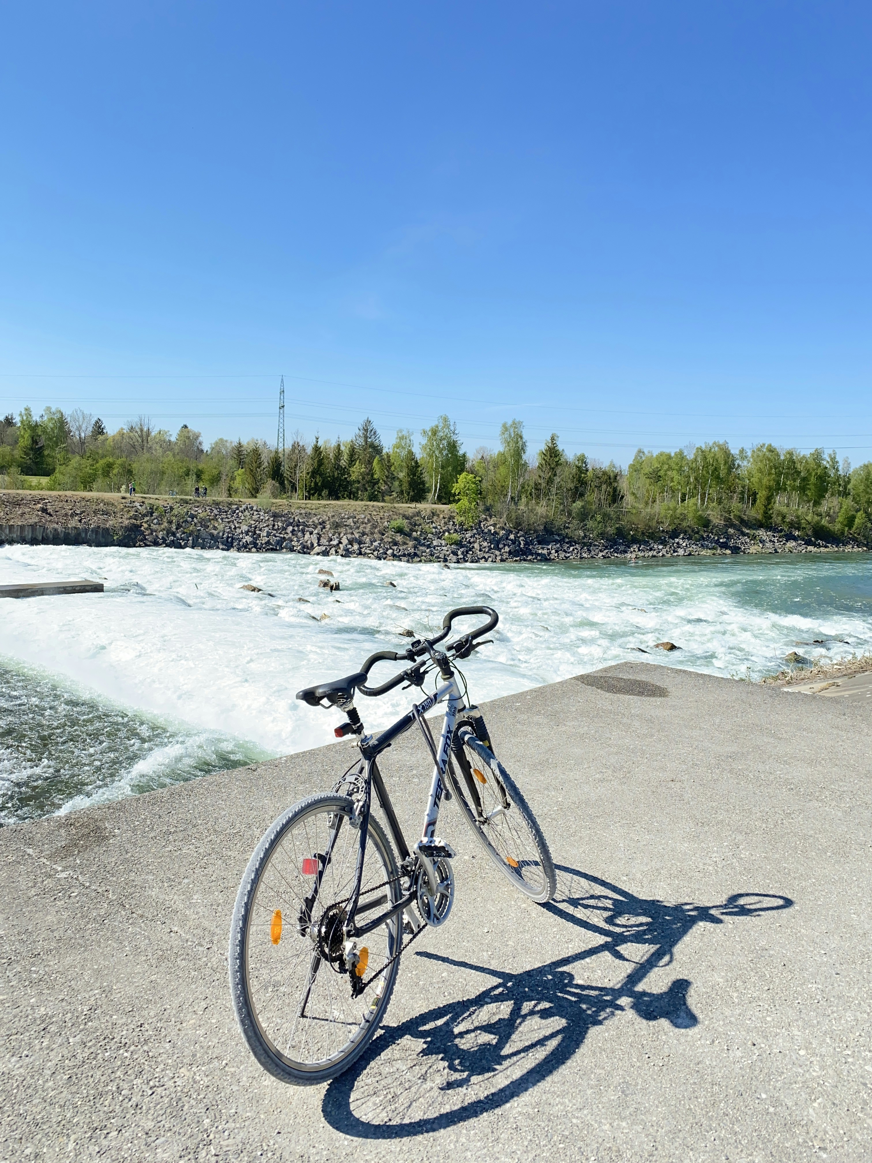 Mountain bike parked on a concrete ledge overlooking rushing water and lush greenery.