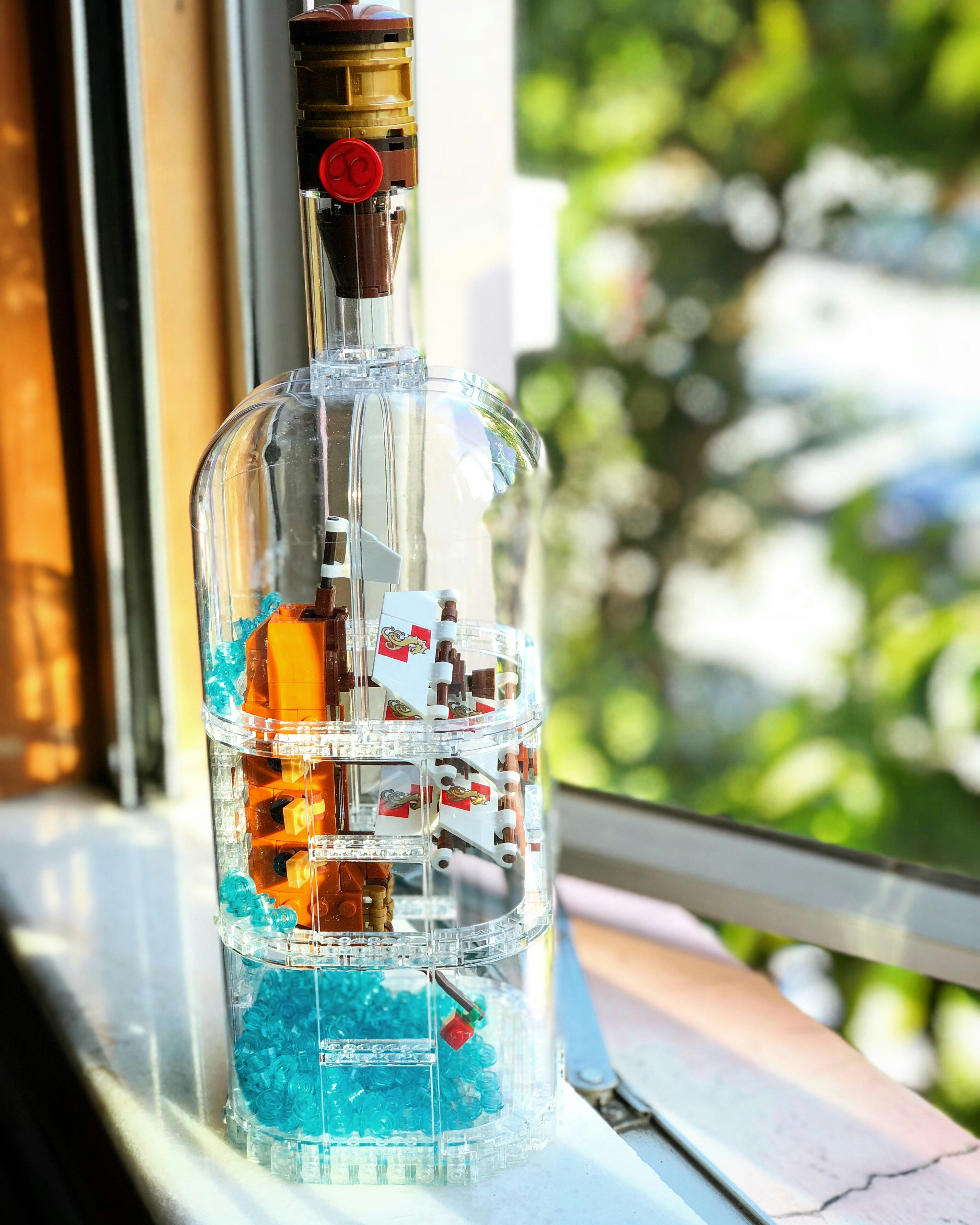 Intricate miniature scene inside a glass bottle featuring colorful elements and blue gravel, illuminated by natural light from a nearby window.