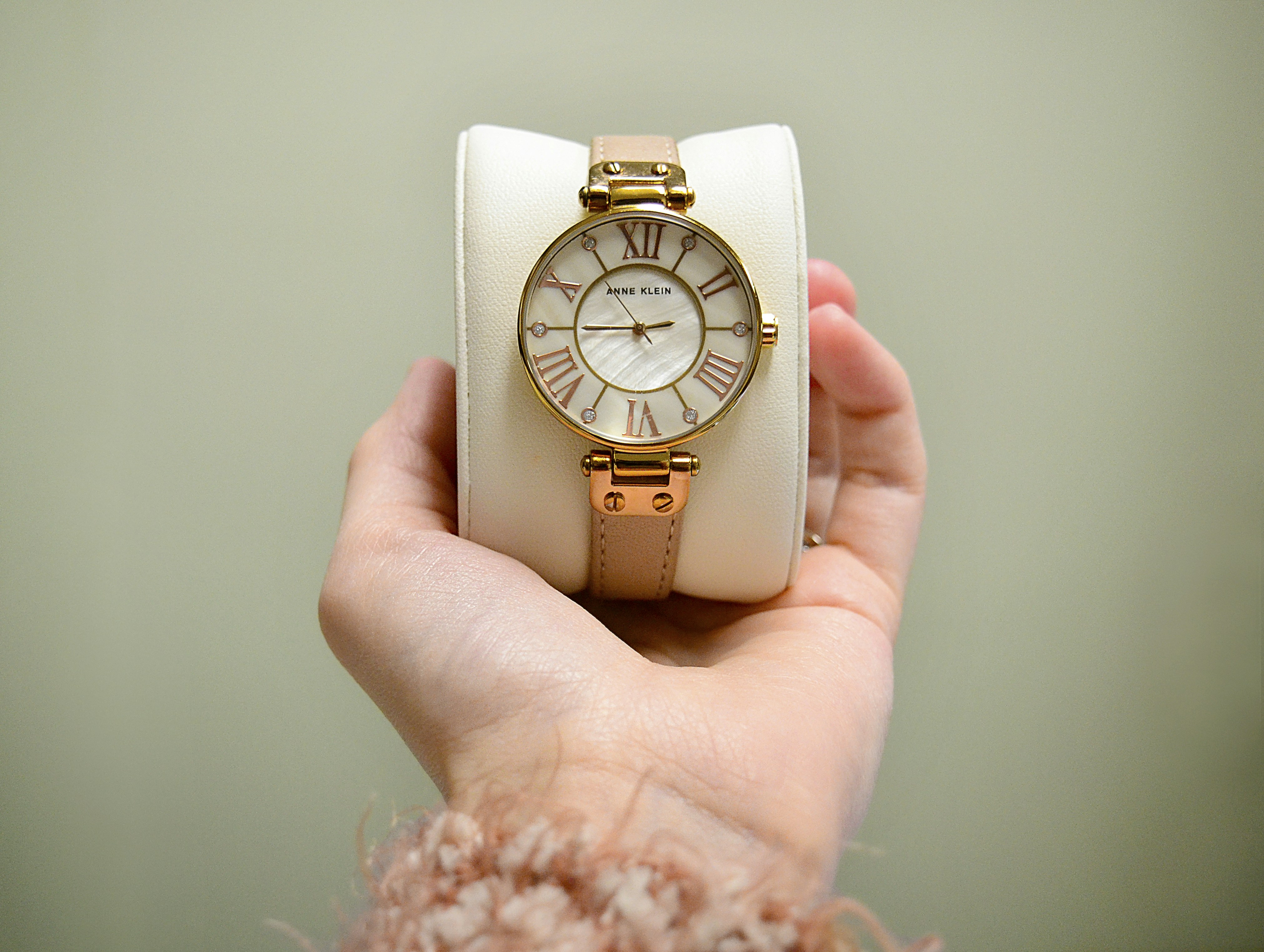 Gold-accented watch displayed on a soft cushion, held by a hand against a muted background.