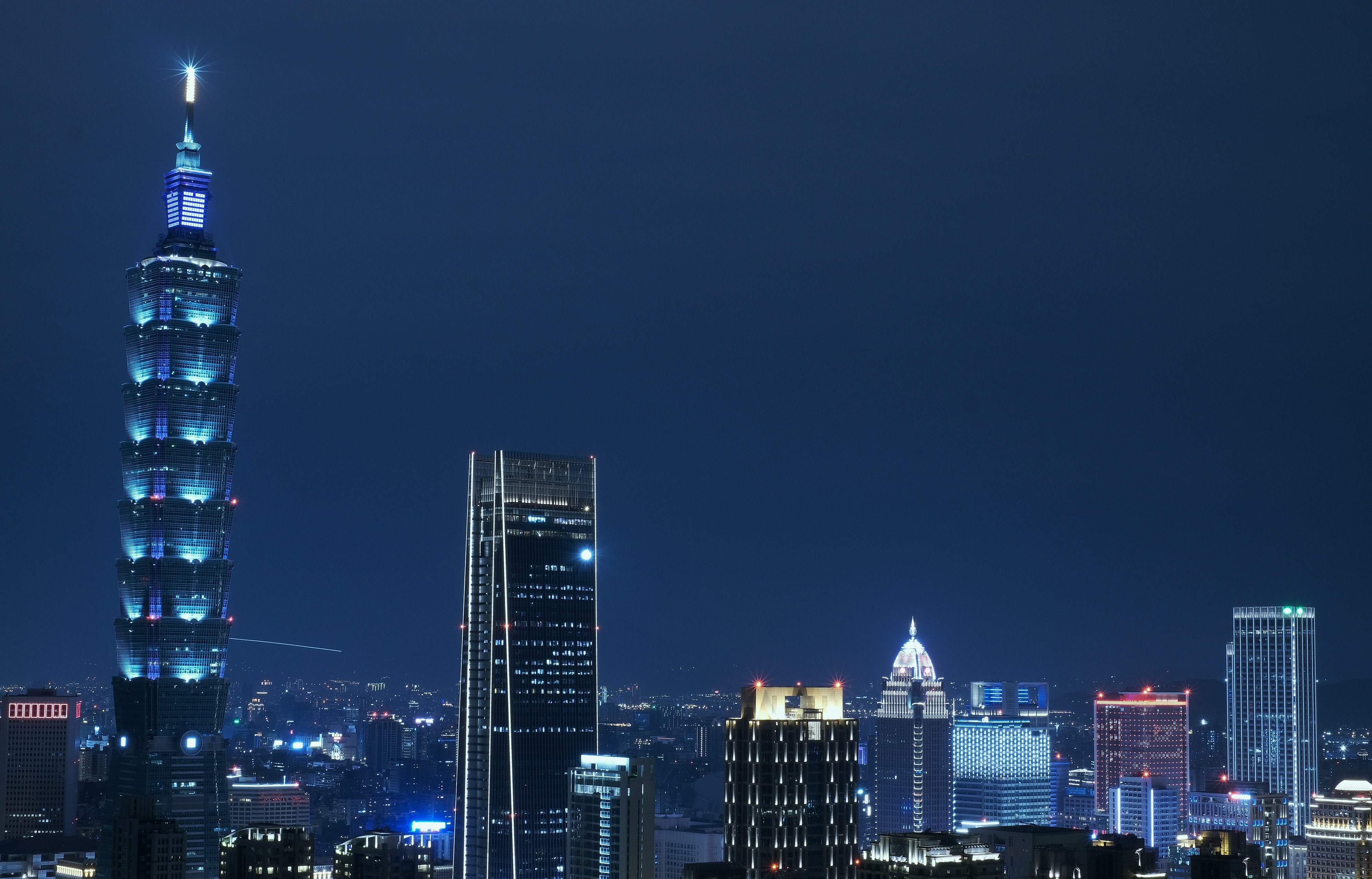 Illuminated skyscrapers against a dark sky, featuring Taipei 101 as the focal point. The vibrant cityscape showcases modern architecture and urban life.