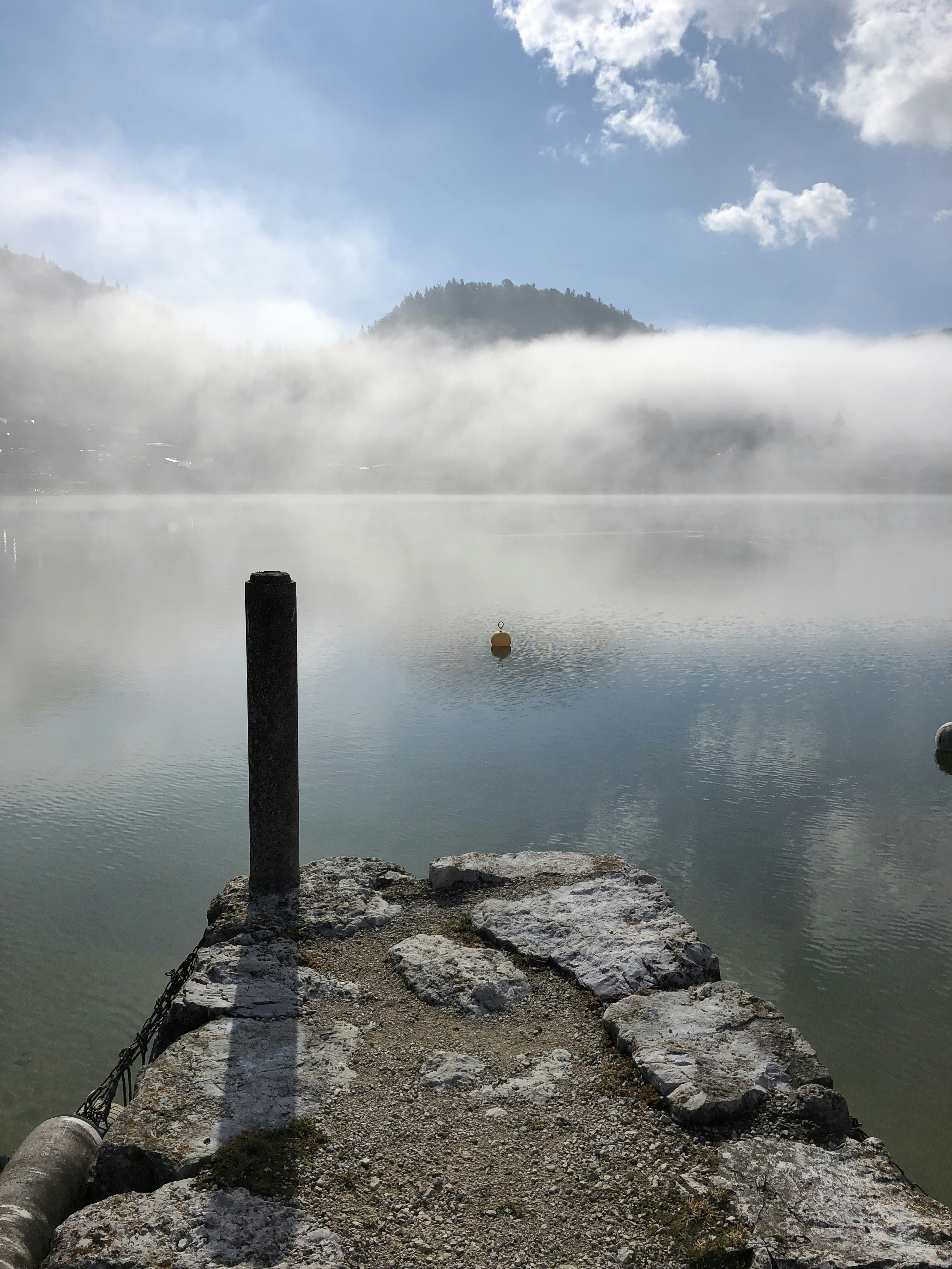 A serene lakeside view with a foggy backdrop and a buoy floating gently on the water's surface.