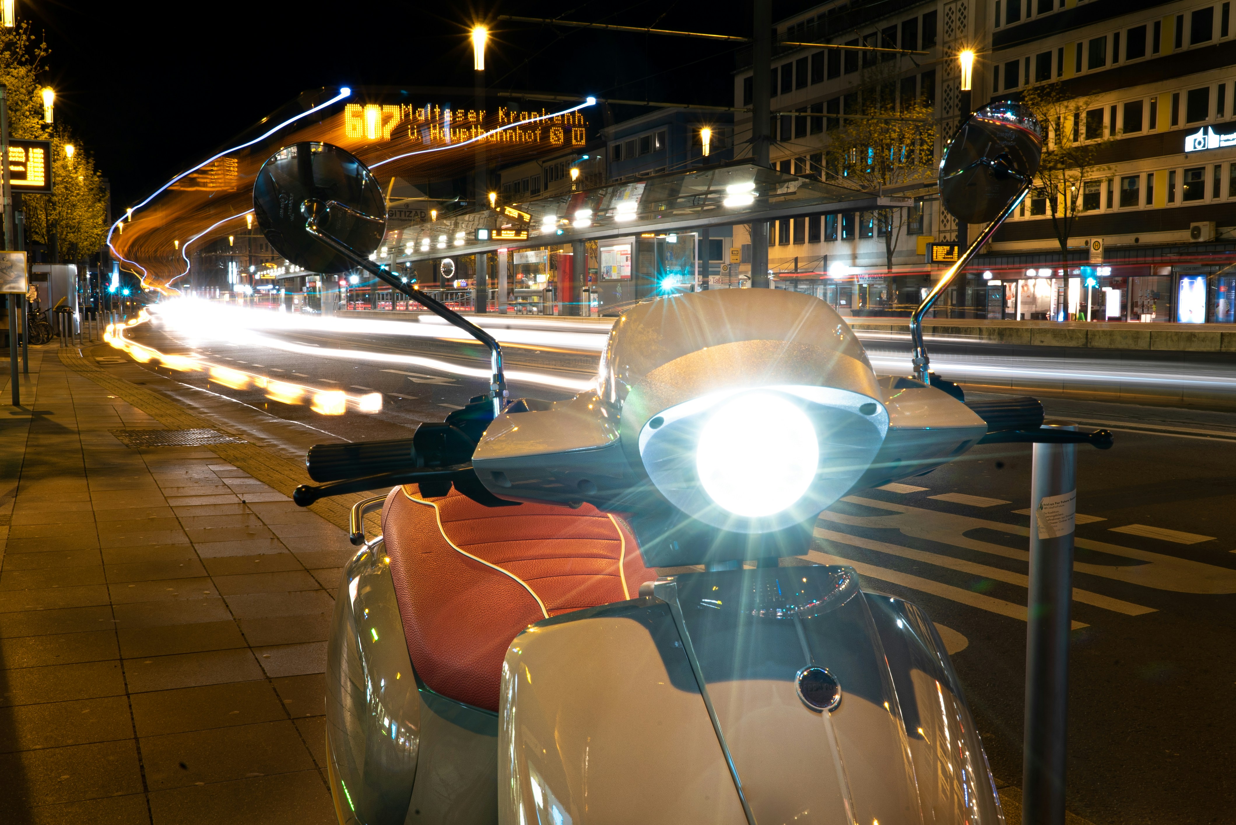 Electric scooter with bright LED front light against a backdrop of light trails on a city street at night.