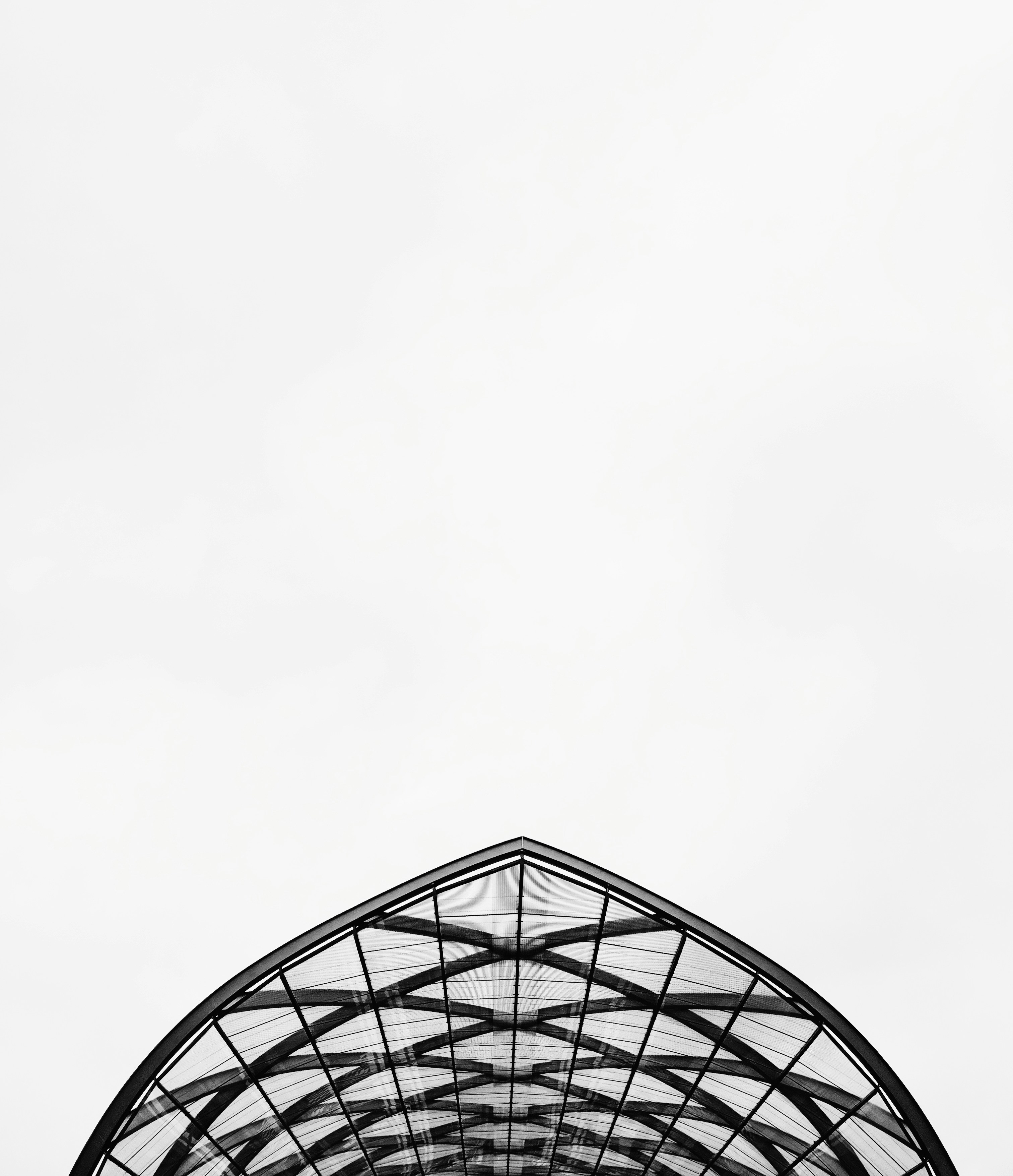 Geometric glass structure viewed from below, showcasing intricate patterns against a blank sky.