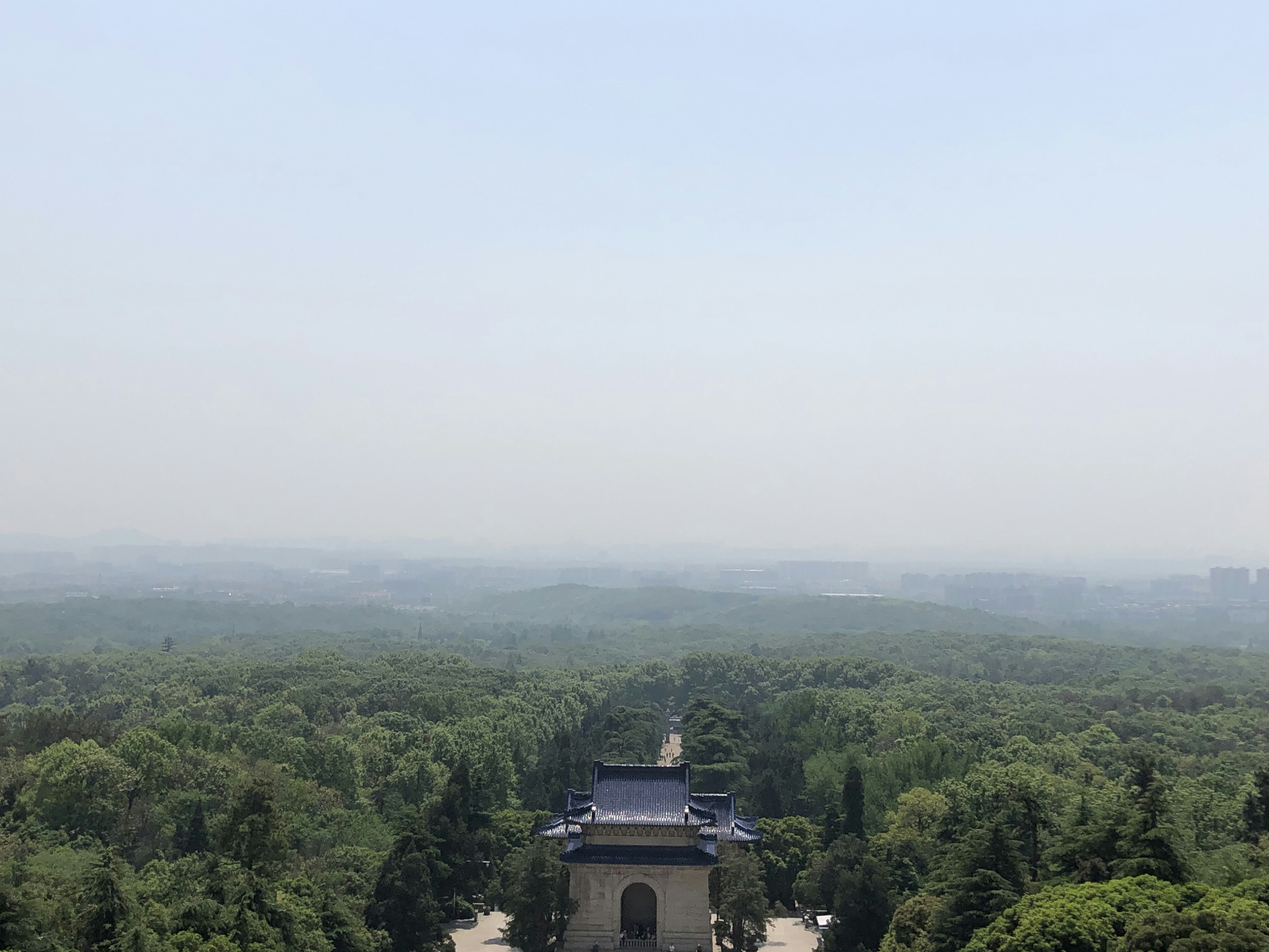 A historical archway framed by lush greenery, set against a hazy backdrop of distant hills. The scene evokes tranquility and a connection to nature.