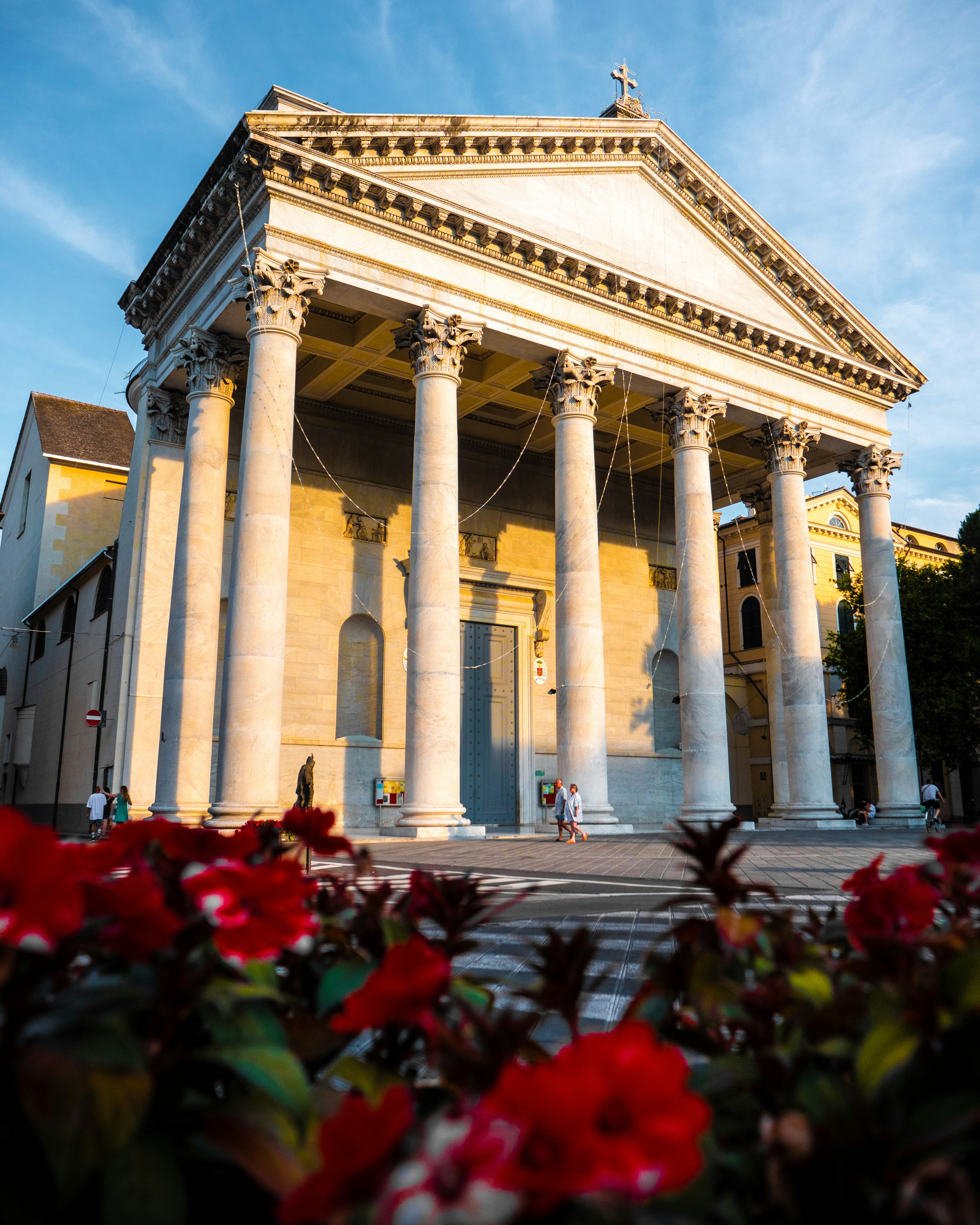 Neoclassical building with grand columns bathed in golden hour light, framed by vibrant flowers in the foreground.