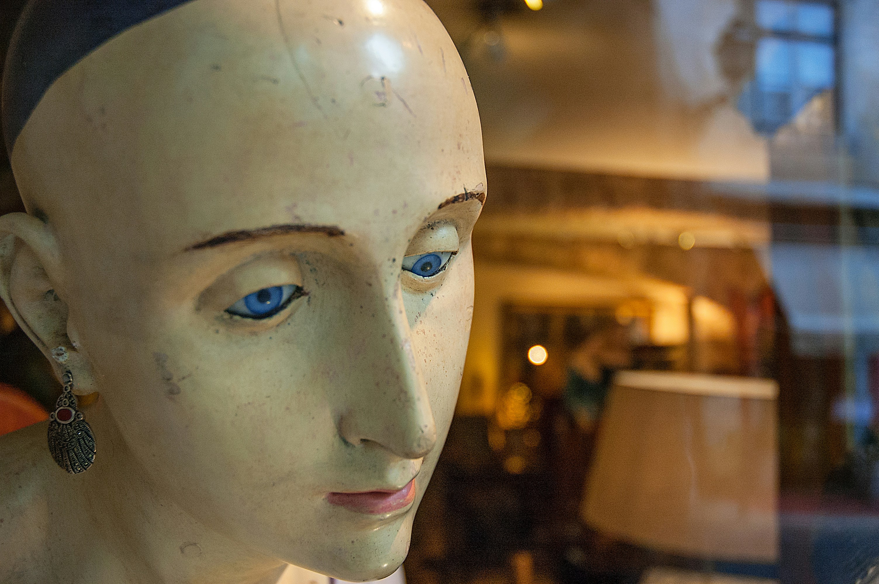 Close-up of a vintage mannequin with striking blue eyes and a subtle expression, reflecting a nostalgic ambiance in a shop window.