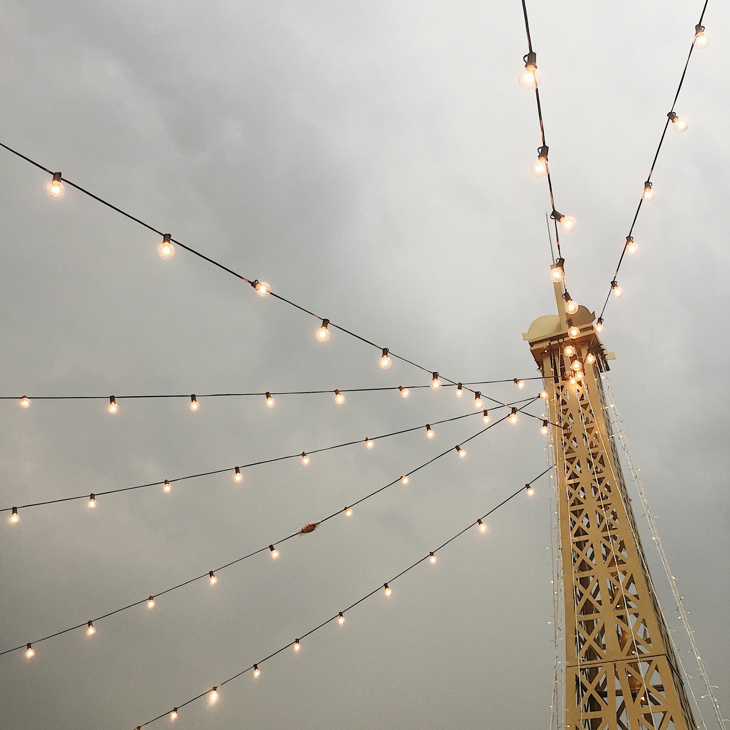 A series of glowing lights stretch across a cloudy sky, anchored by a tall, elegant structure. The interplay of light and shadow creates a dramatic atmosphere.