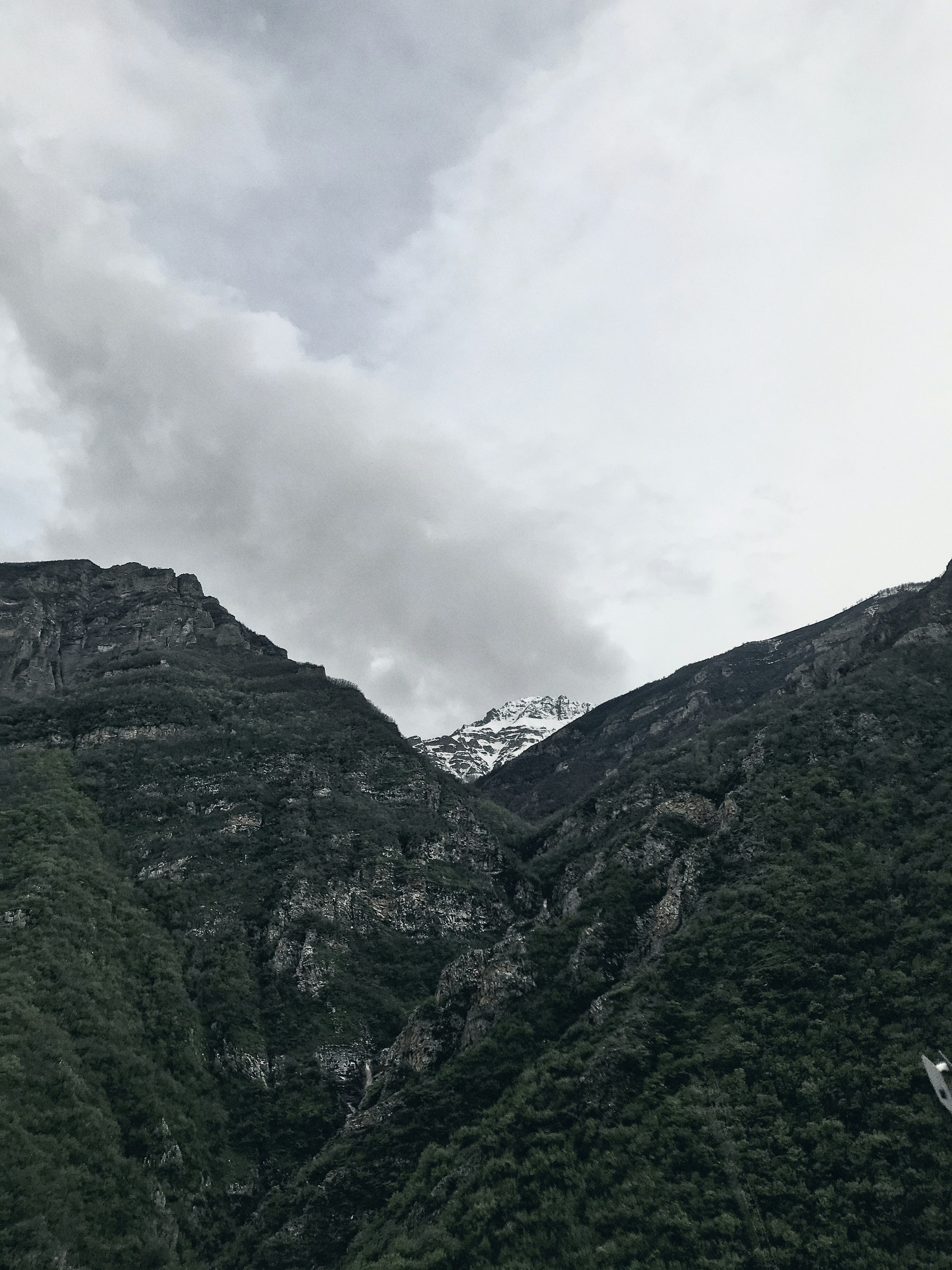 Snow-capped mountains nestled between lush green valleys under a cloudy sky.