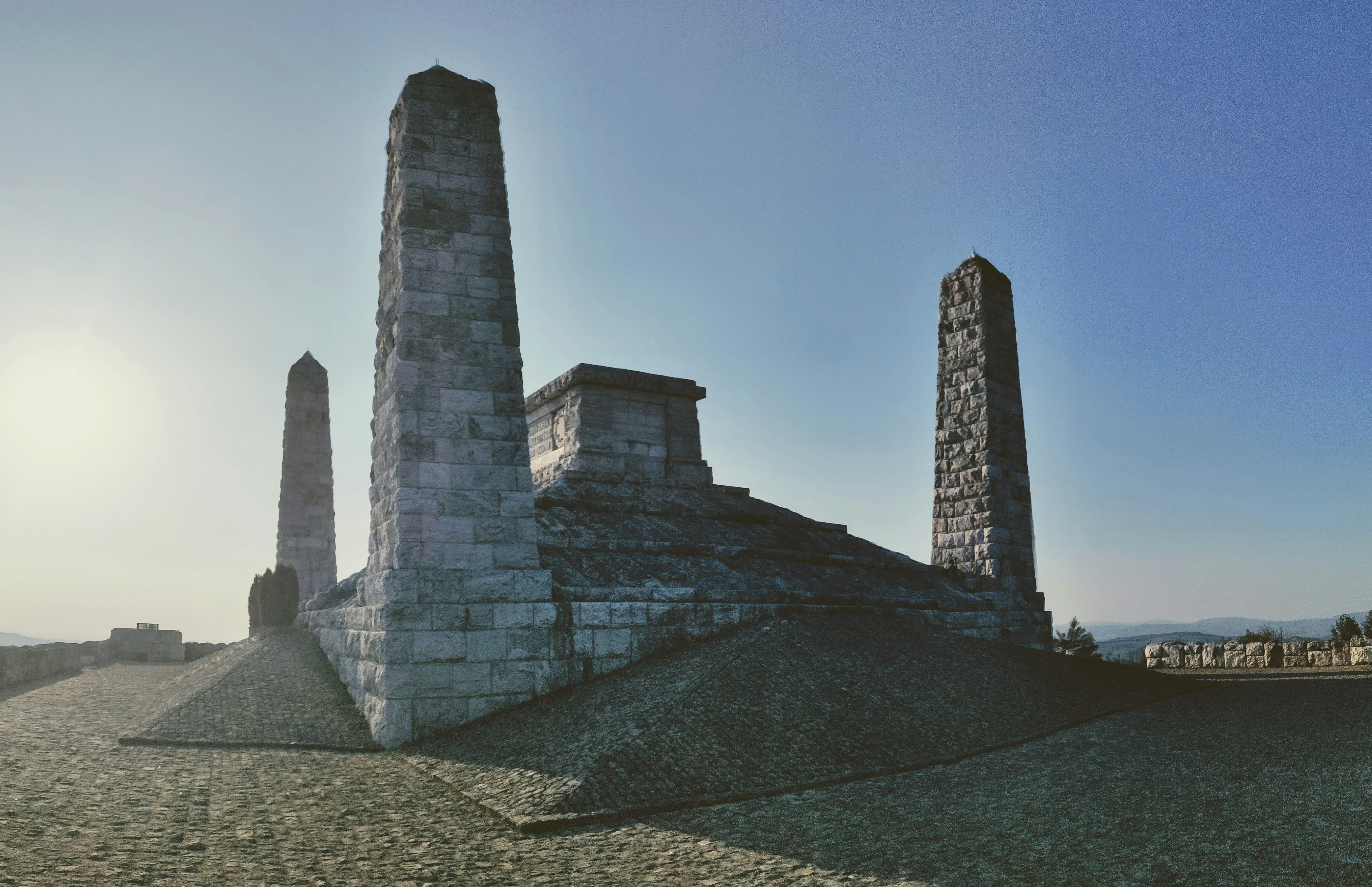 Ancient stone structures casting long shadows on a sunlit dirt field.