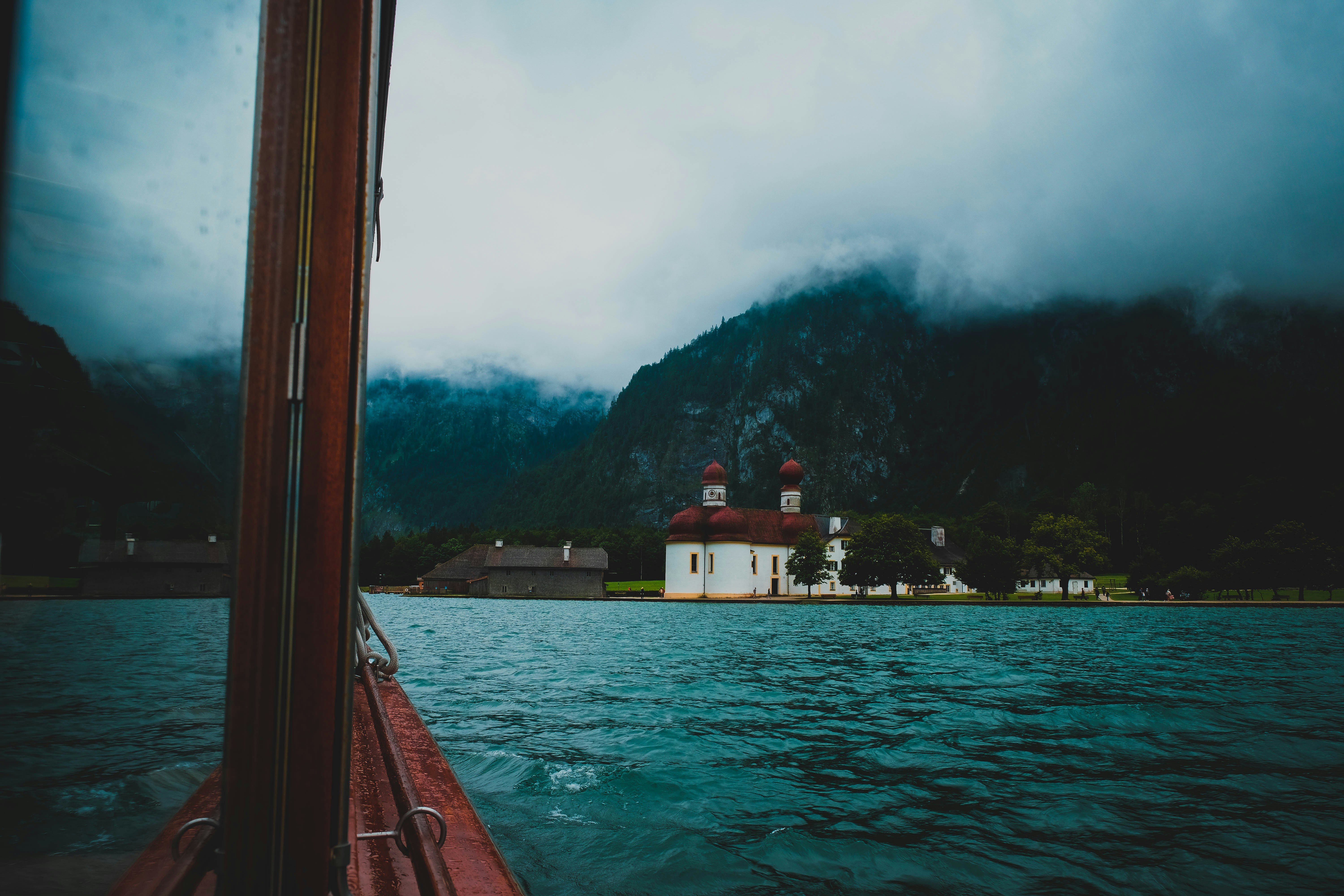 White church with red domes nestled by a mist-covered mountain lake.