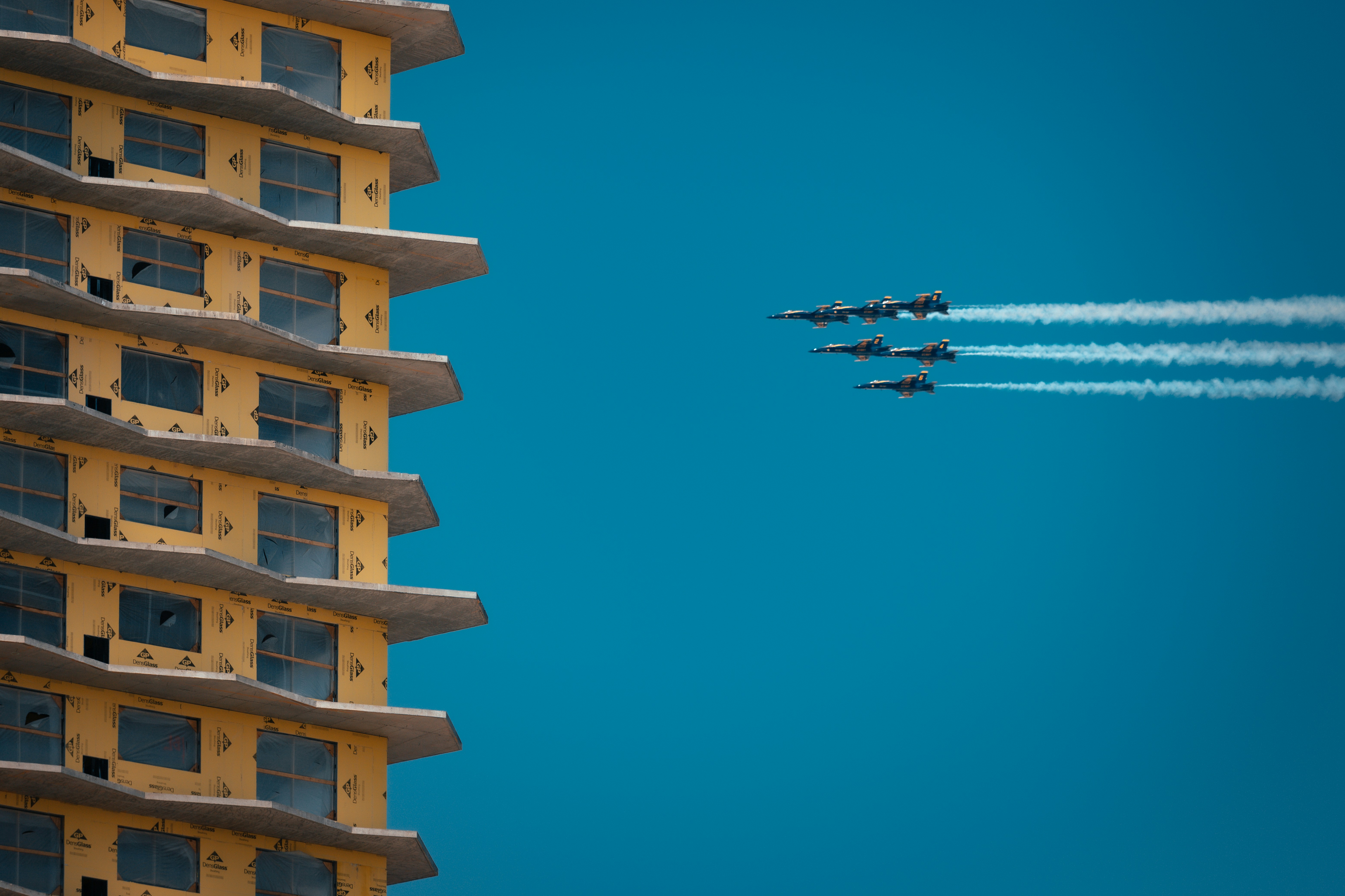 Cerulean Sky Over a Stacked Façade: Jet Trails Across an Urban Edge