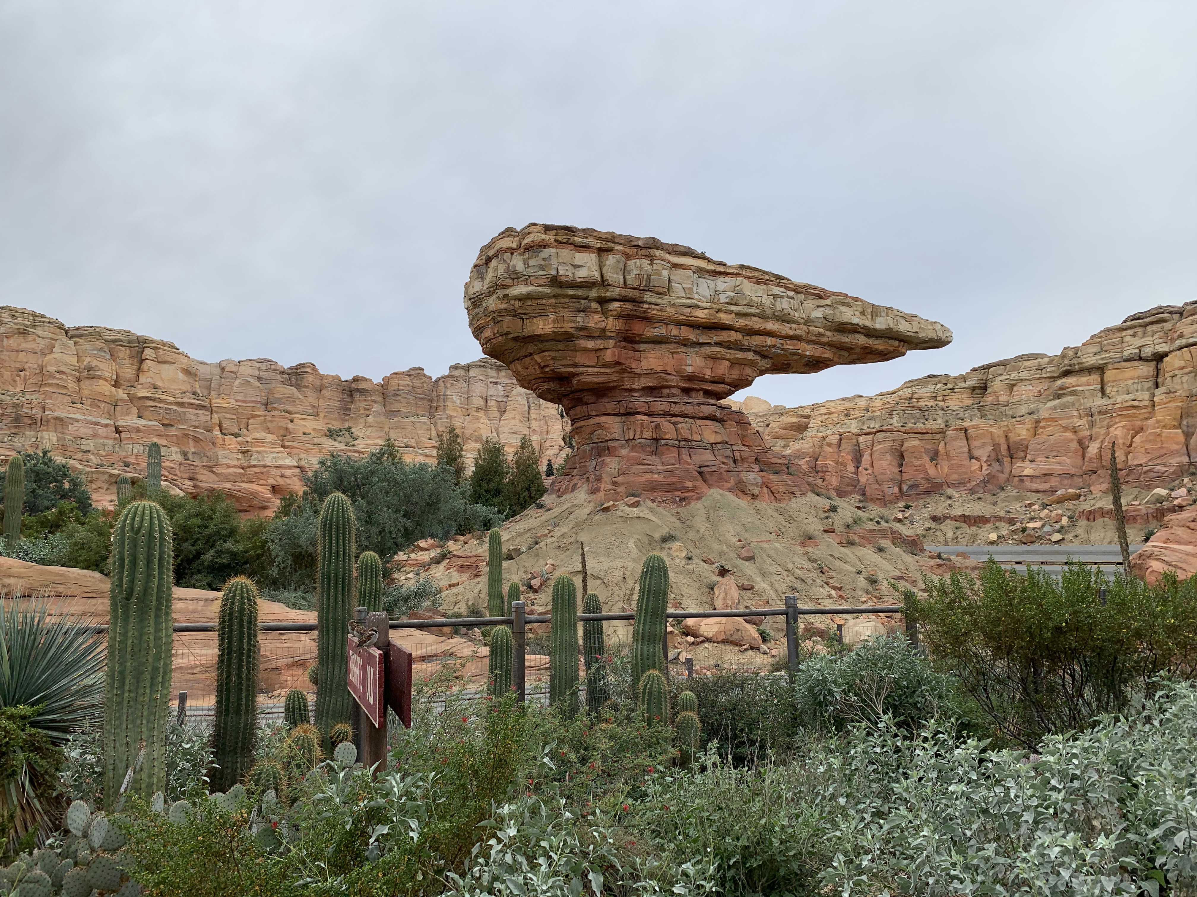 Unique rock formation resembling a balancing structure amid desert vegetation under a cloudy sky.