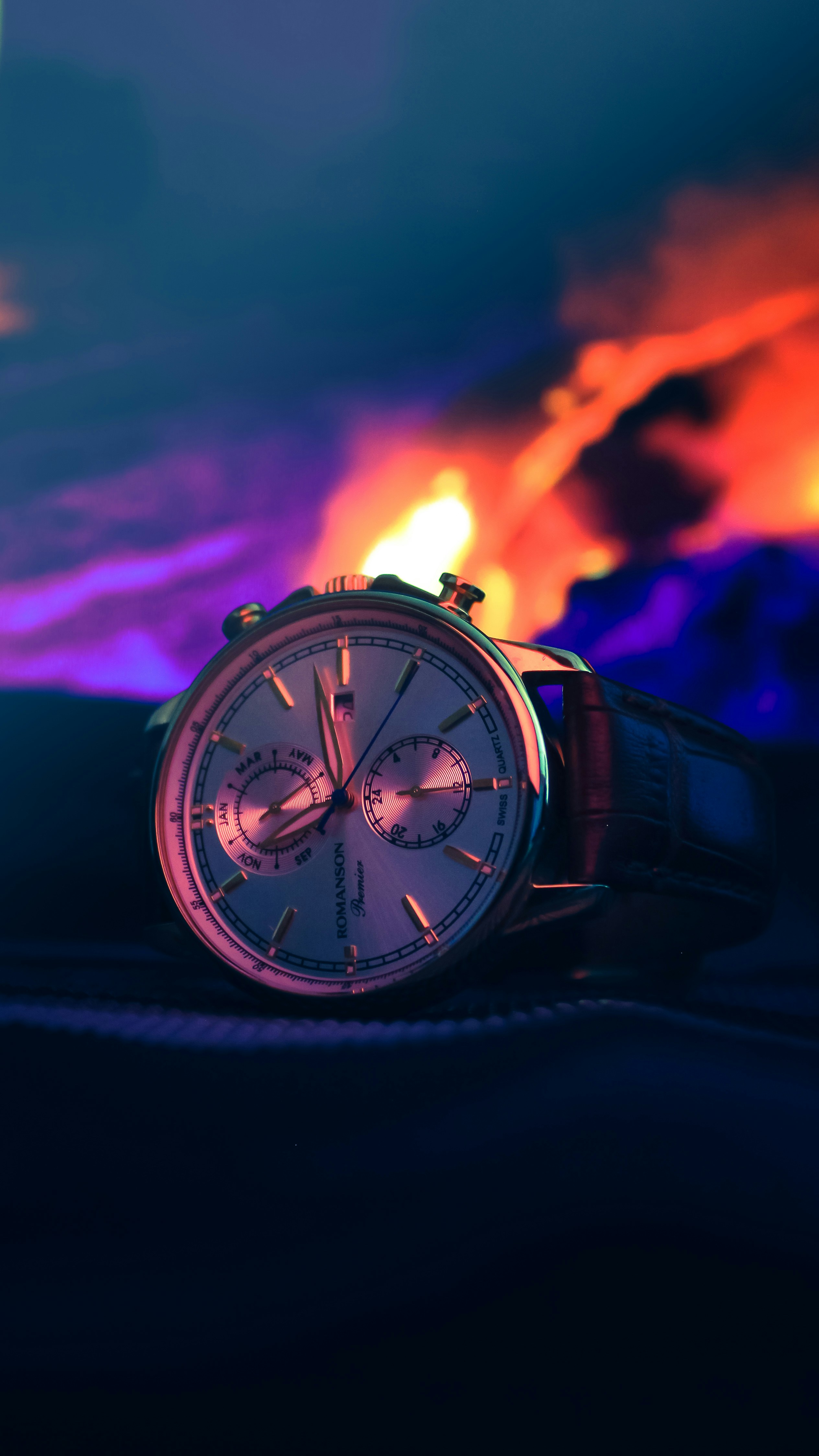 A sophisticated watch rests on a textured surface, illuminated by vibrant colors reminiscent of molten lava in the background.