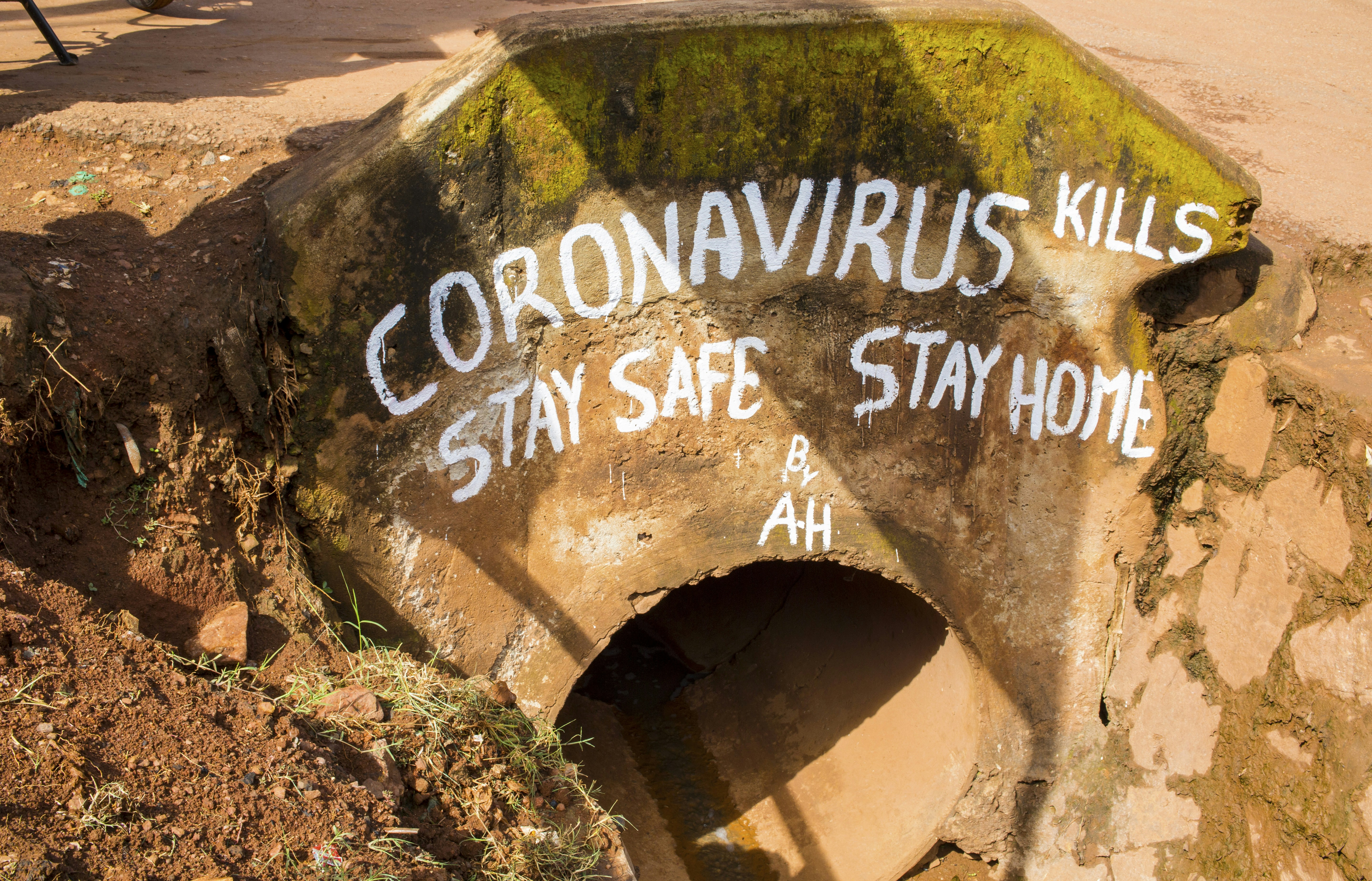 A concrete tunnel entrance with painted COVID-19 safety messages urging caution.
