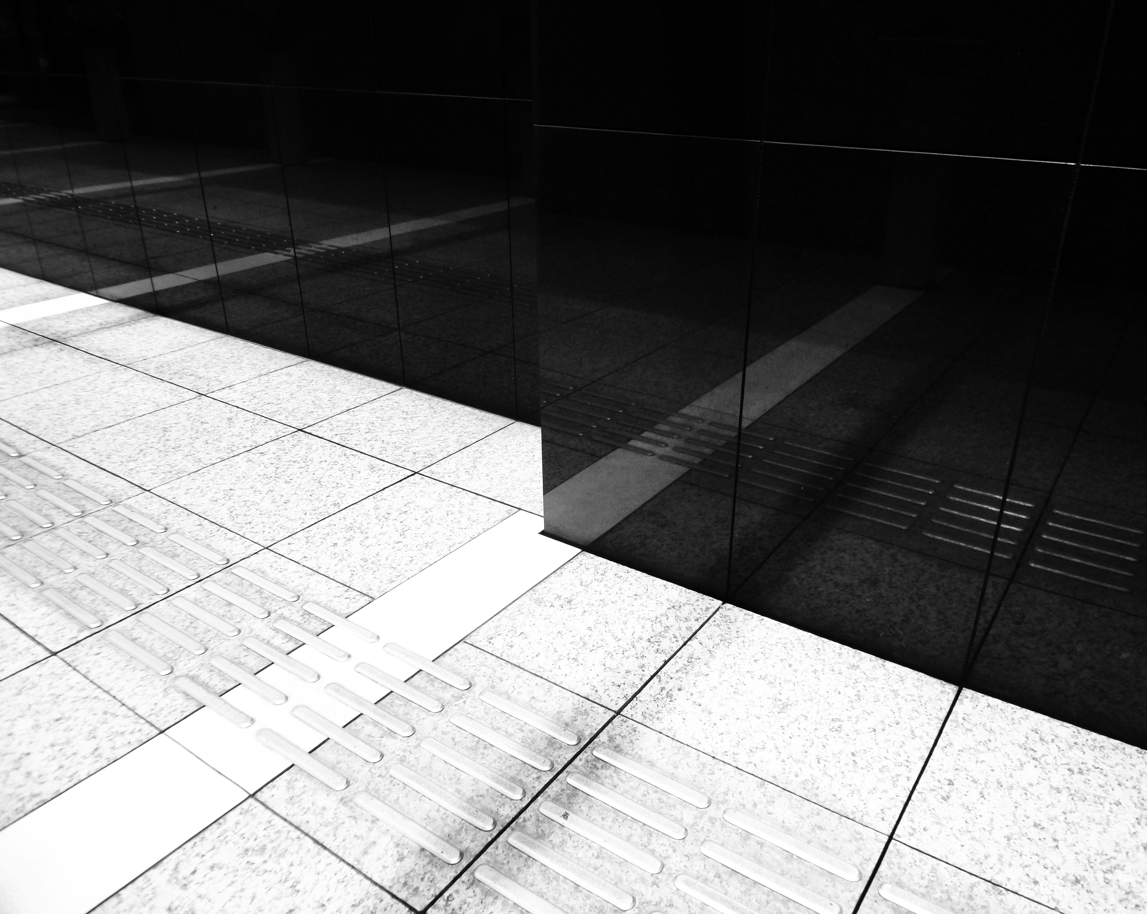 Monochromatic scene showcasing textured tiles and a reflective black surface, emphasizing the interplay of light and shadow.