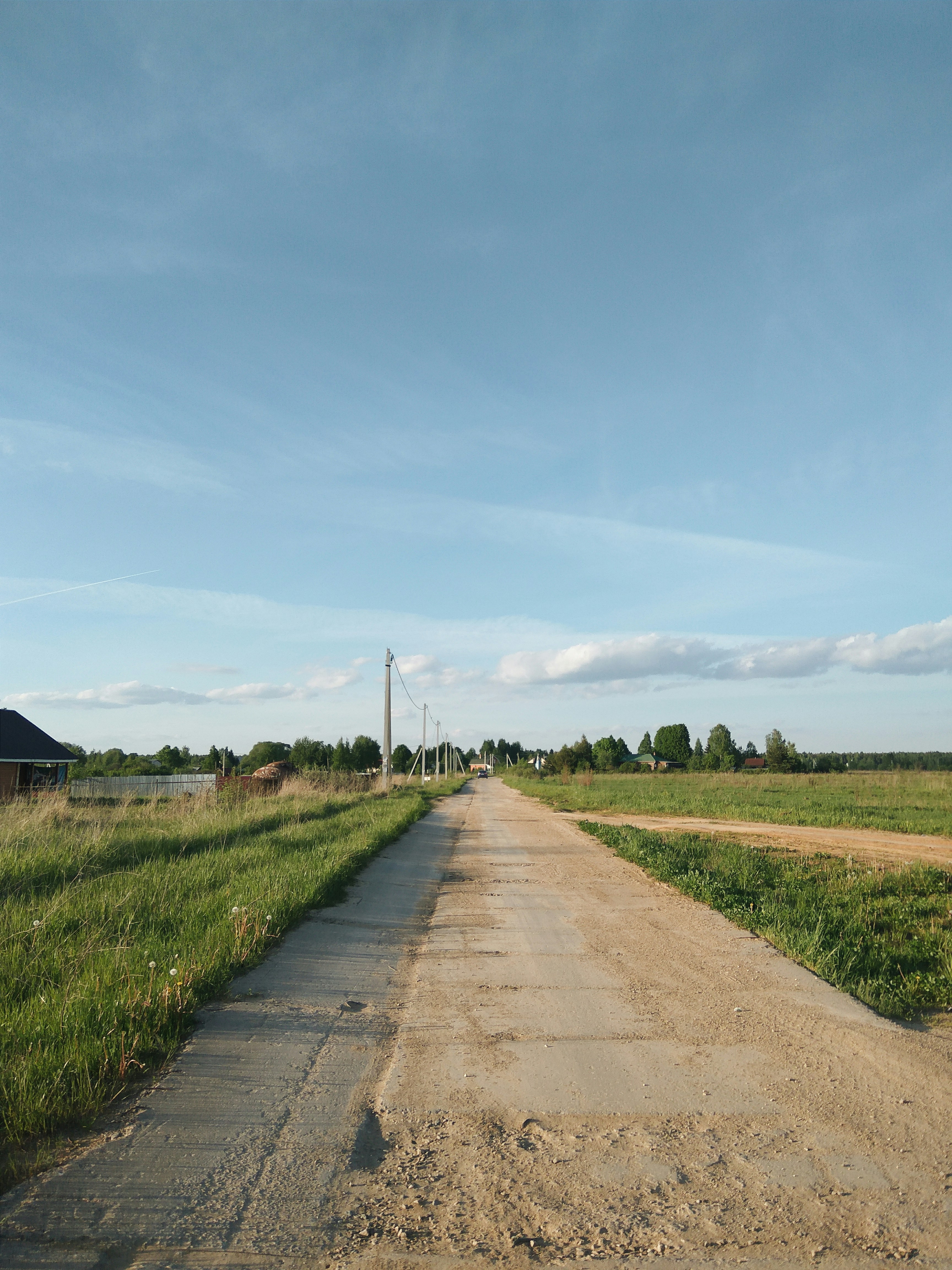 Gravel and concrete pathway leading into a serene landscape, flanked by green grass and distant trees under a clear blue sky.