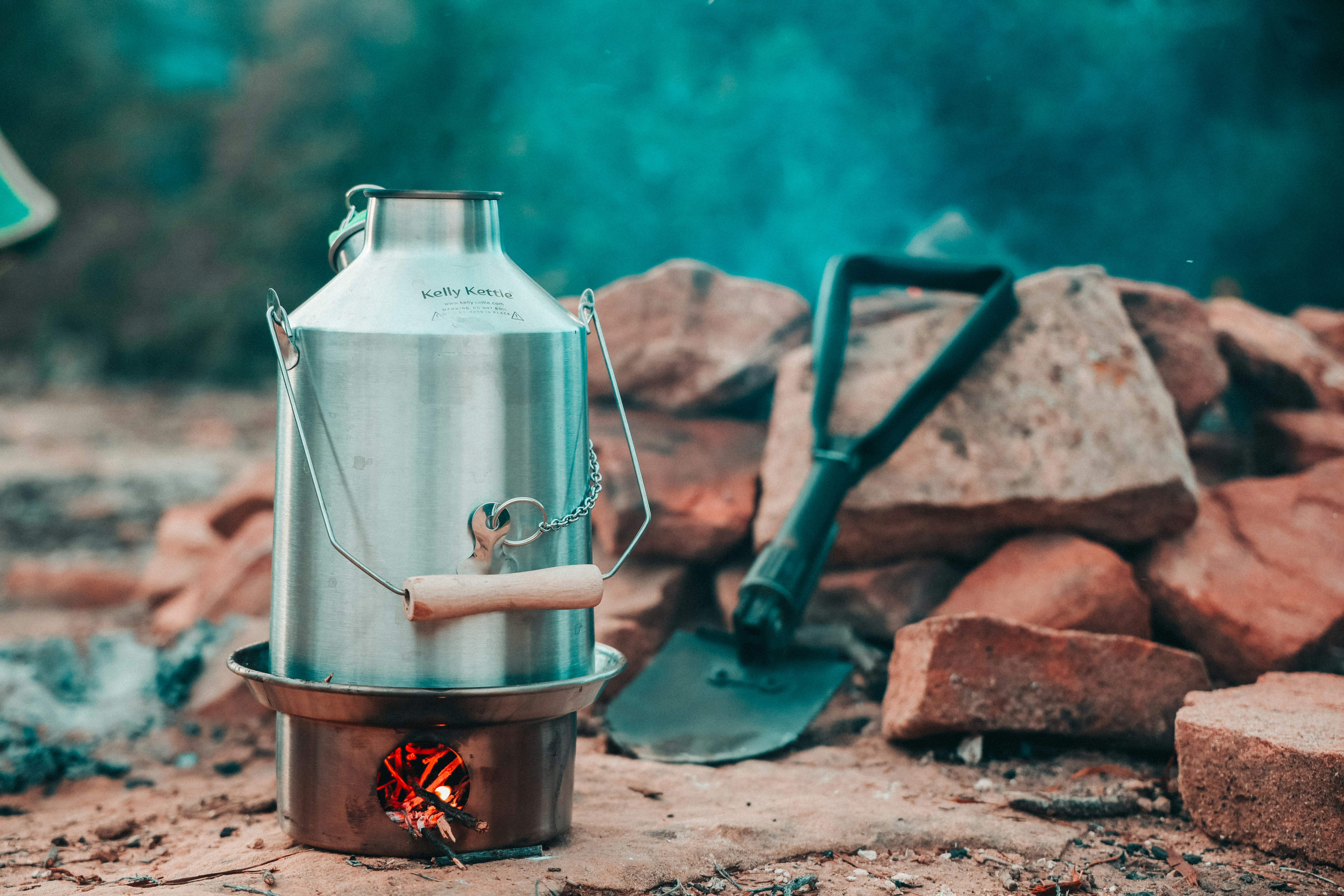 Campfire Concoction: A Metal Can and Shovel amid Ember-Coiled Stones