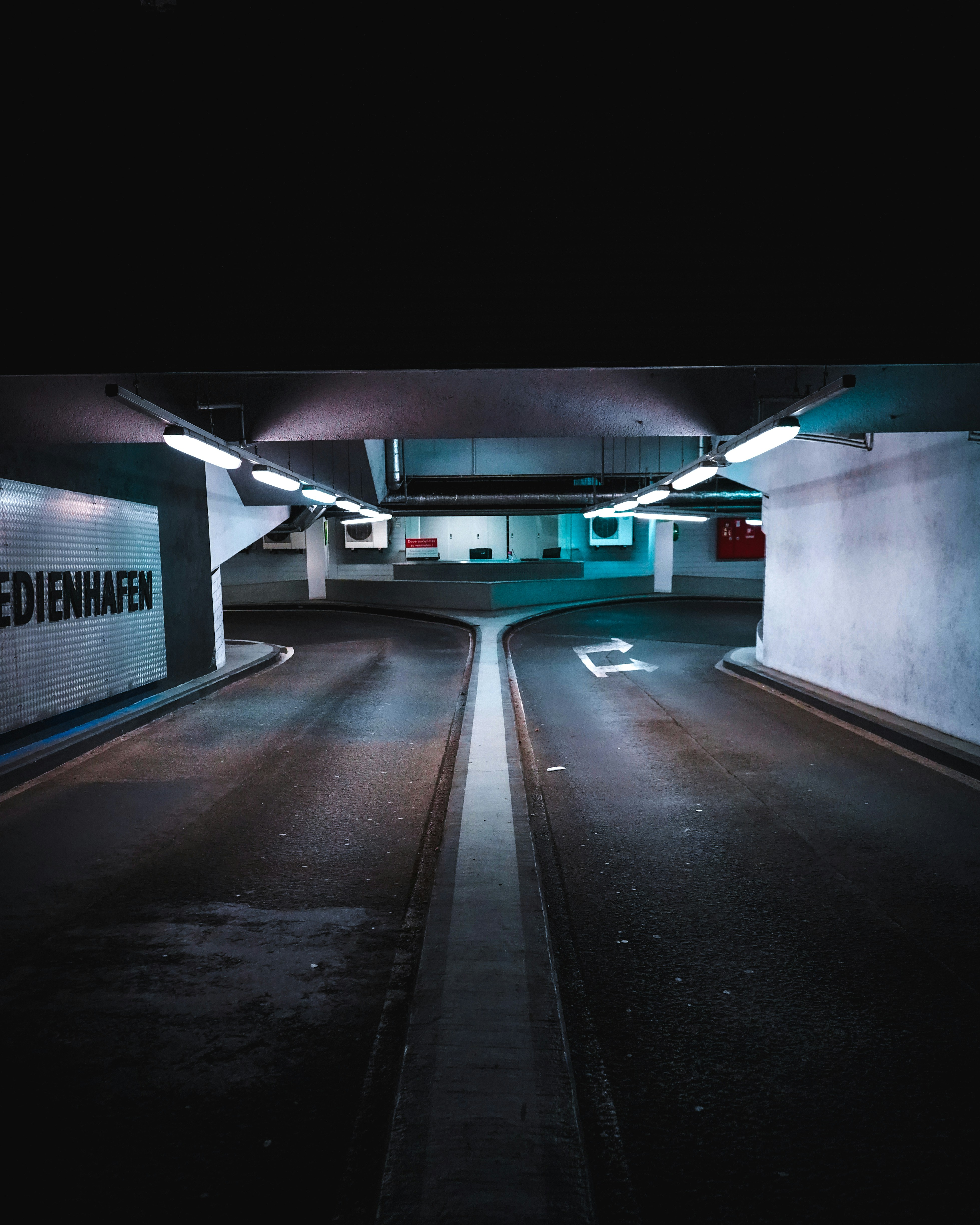 Dimly lit parking garage with a winding path and illuminated signage. The atmosphere evokes a sense of mystery and solitude.