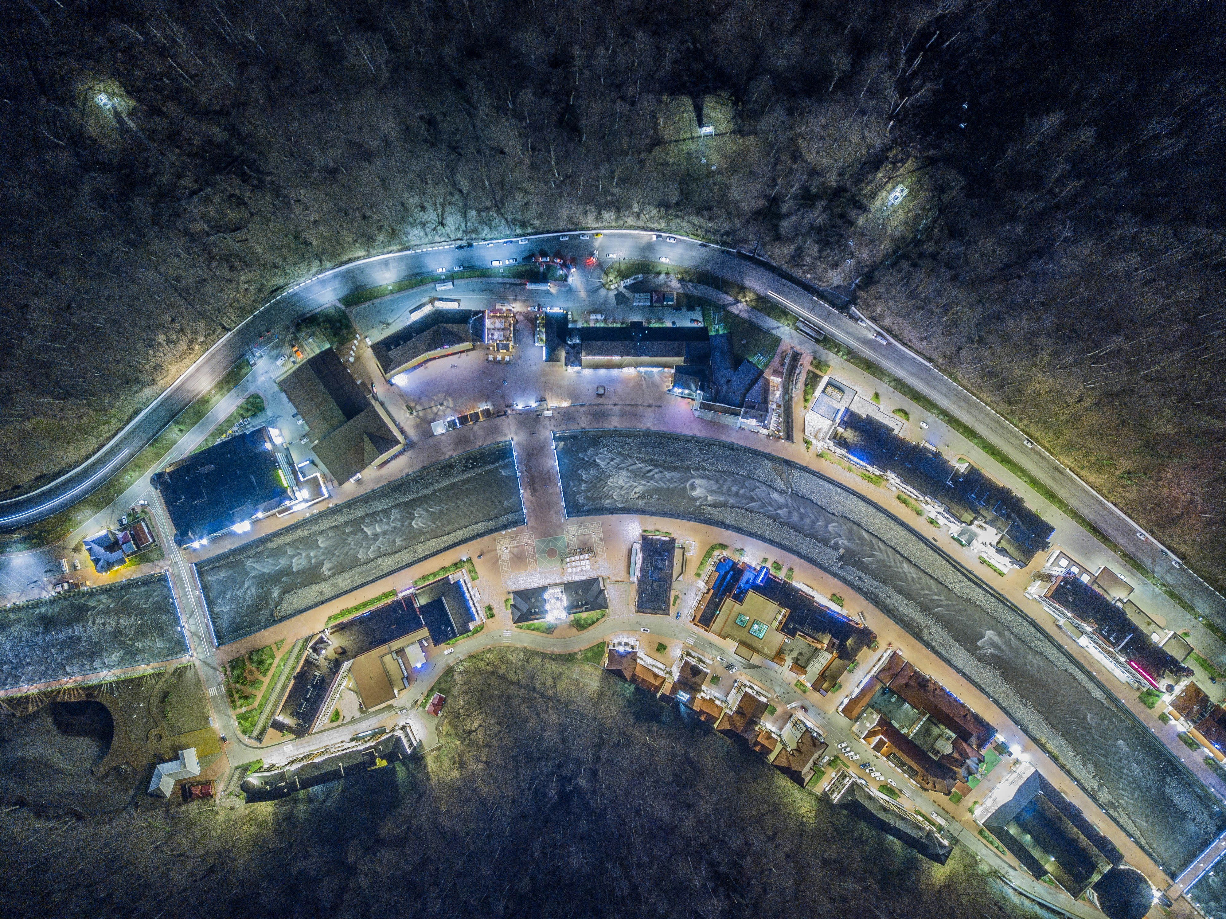 Aerial view of a mountain village at night with illuminated roads and buildings amidst surrounding forest.