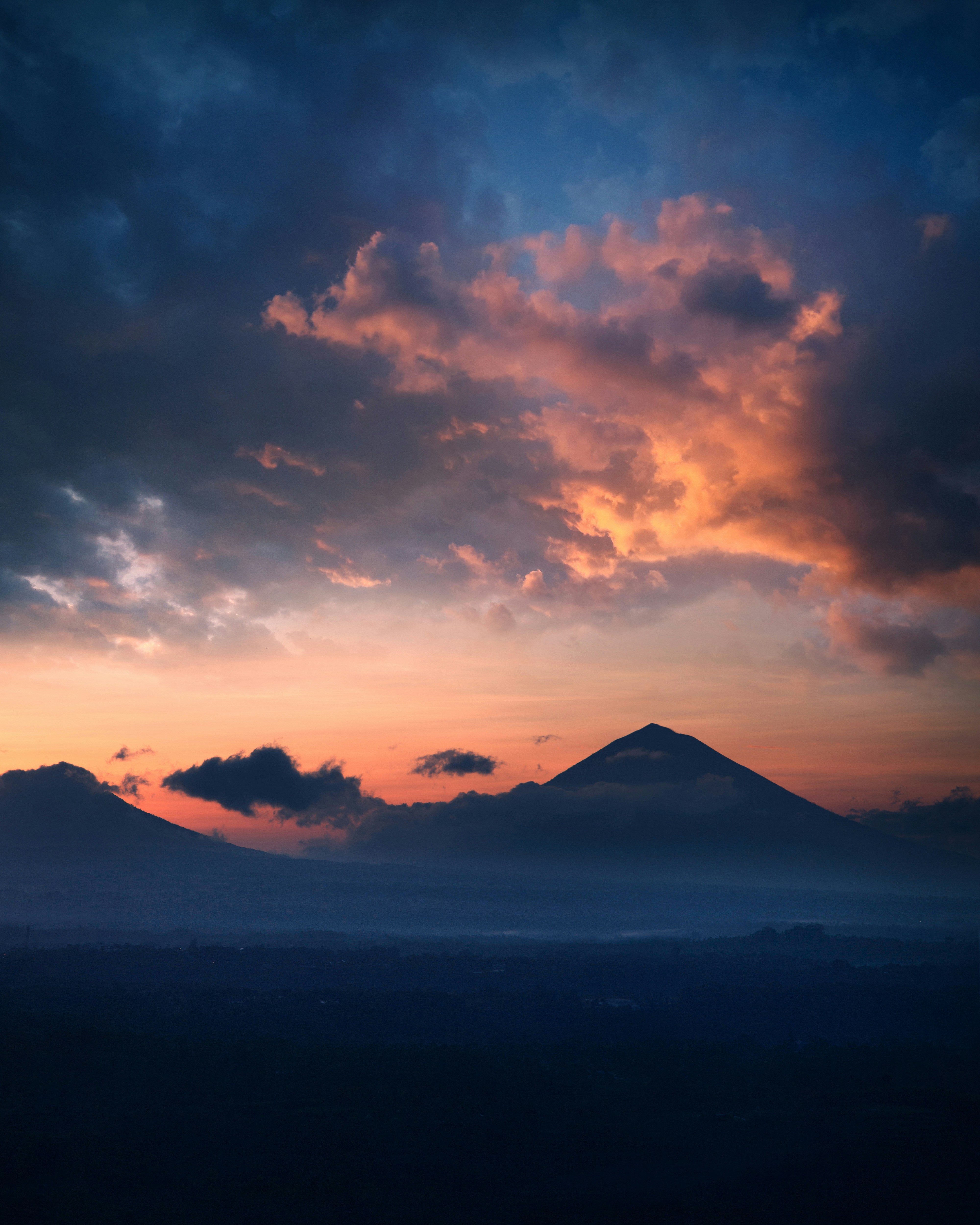 Silhouetted mountains under a vibrant sunset sky with dramatic clouds.