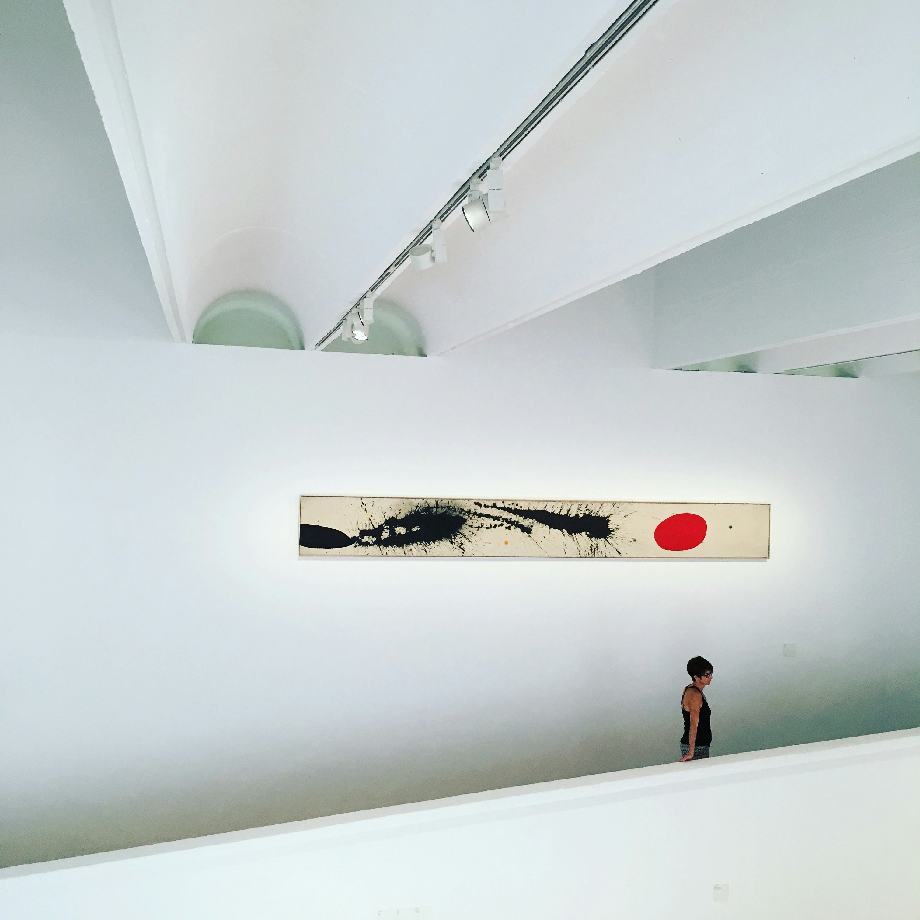 White-Walled Gallery under a Black Ink Panel with a Red Dot: A Solo Figure in Quiet Scale