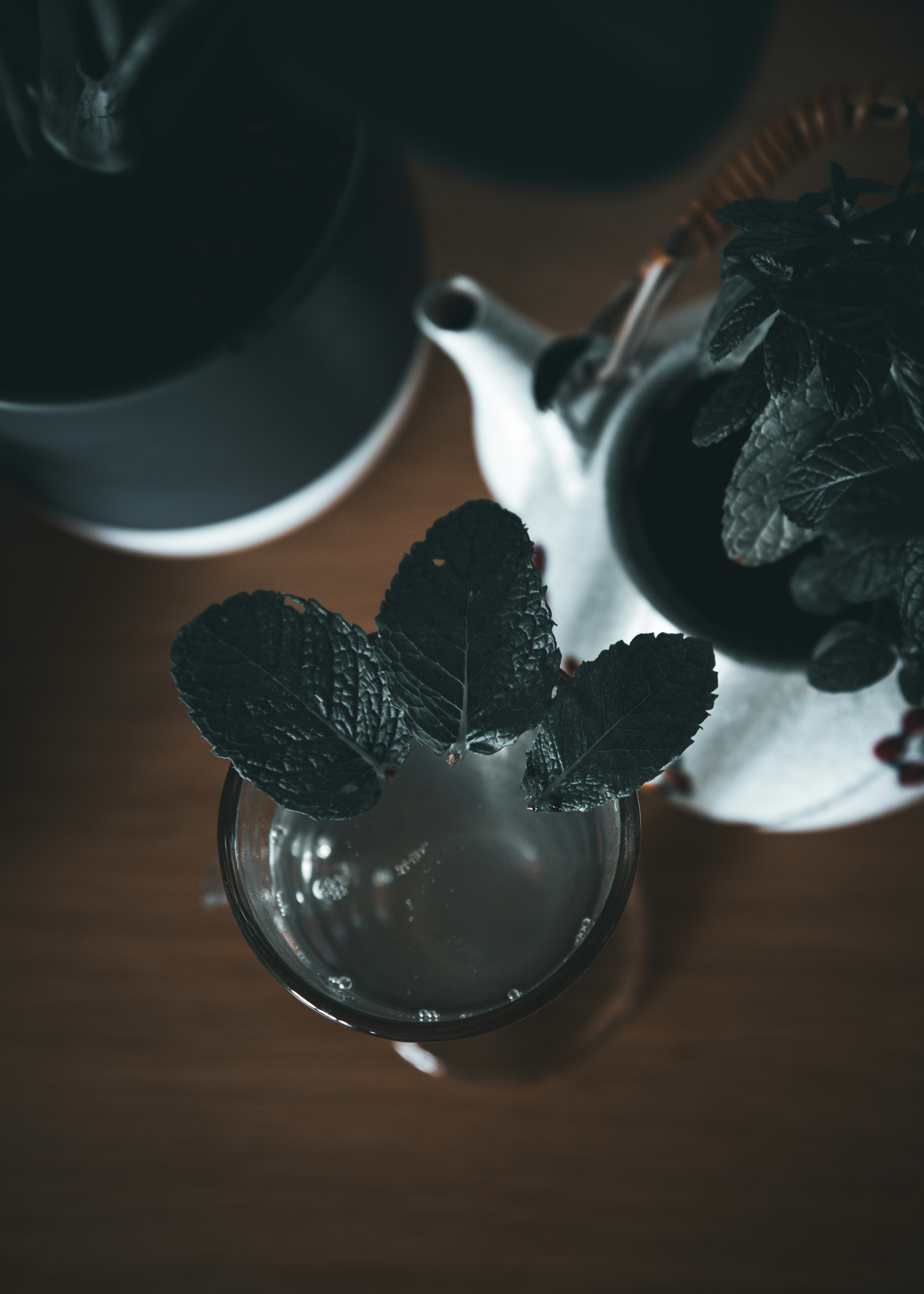A refreshing drink garnished with fresh mint leaves, set against a wooden surface with a teapot and plant in the background.